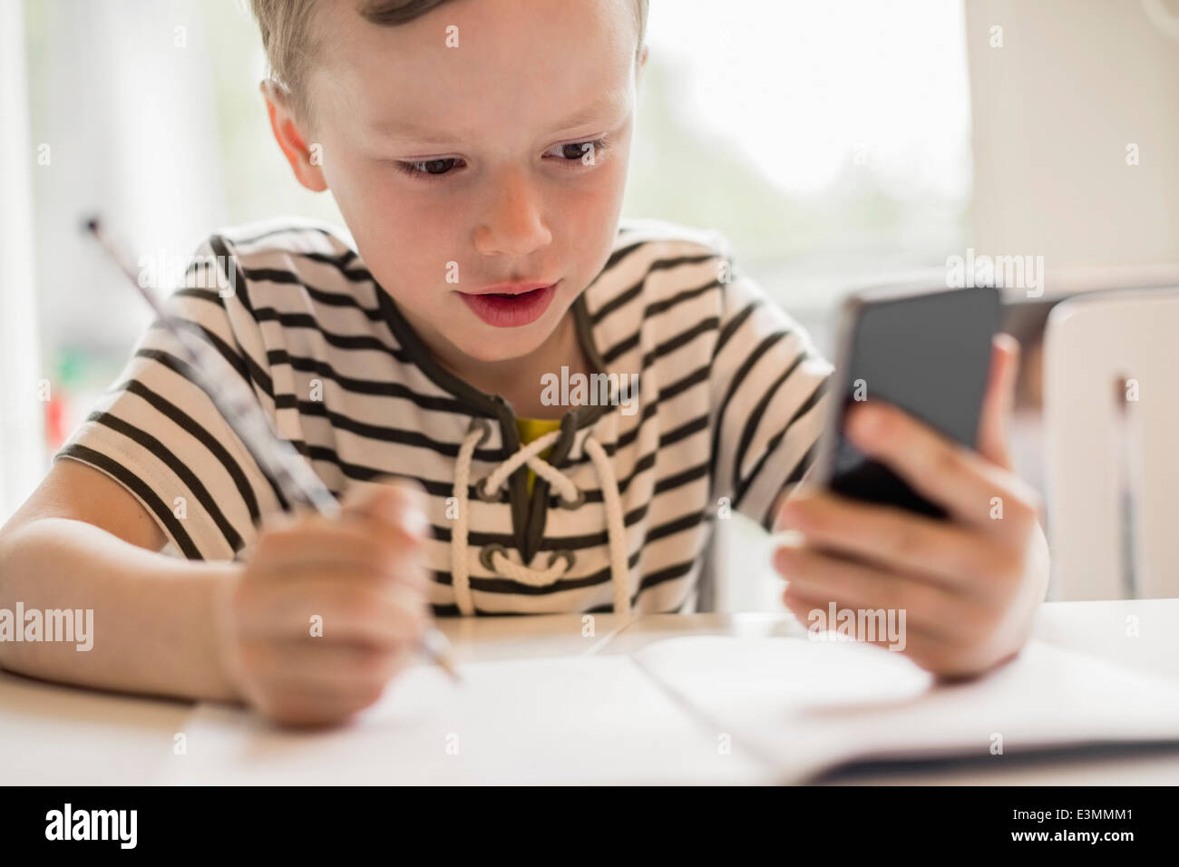 Boy using smart phone while writing at table Stock Photo - Alamy