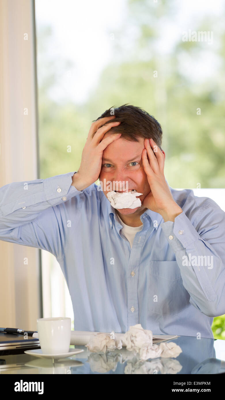 mature man showing stress by biting wad of paper while working from ...