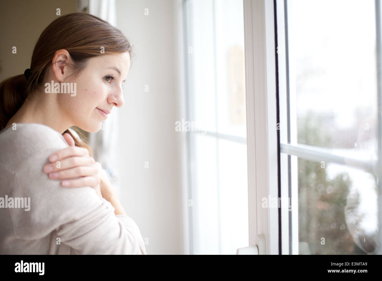 Woman looking from a window of her house on a cold and snowy winter day ...