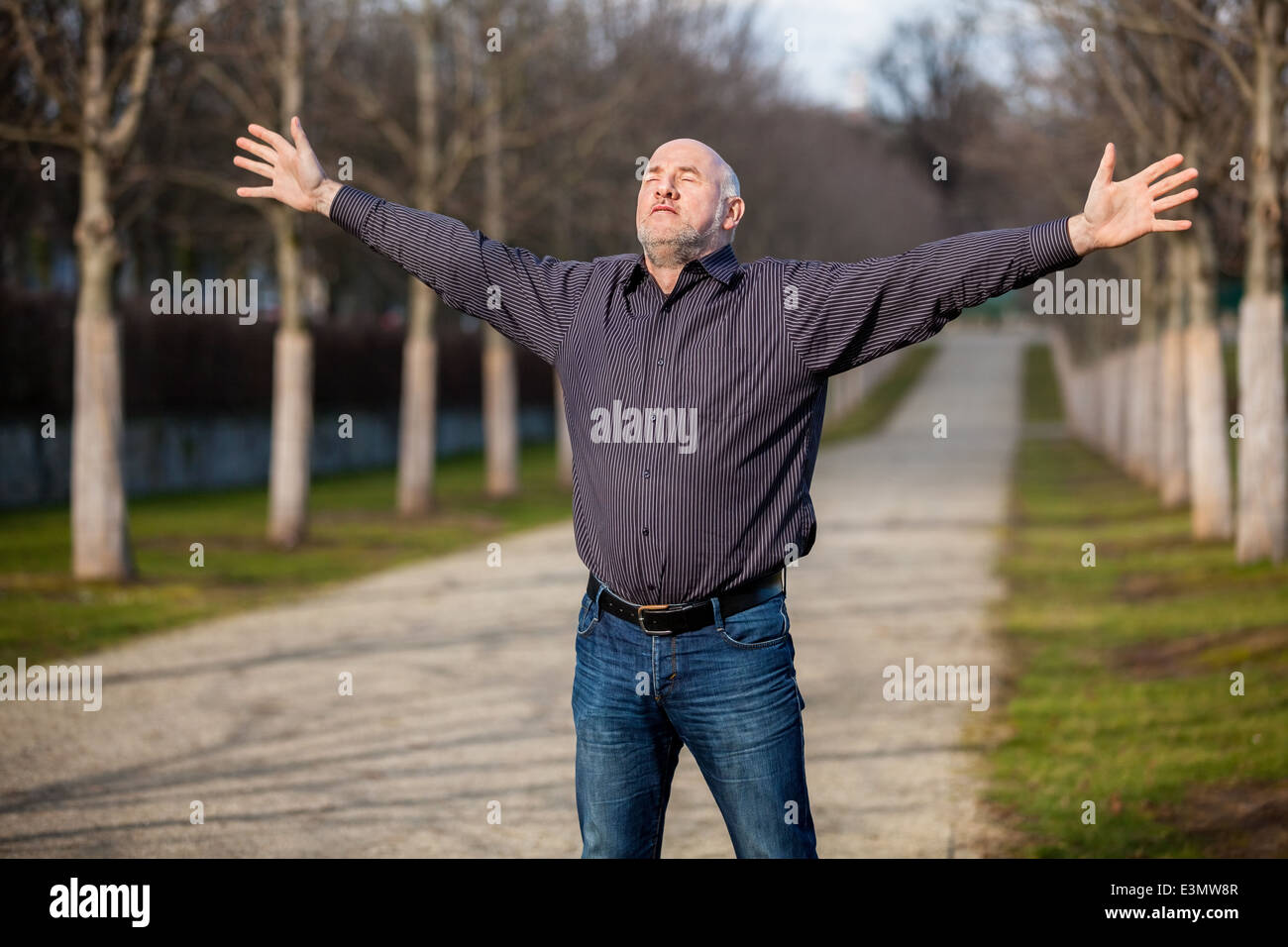Middle-aged man enjoying the sunshine standing with his arms outspread ...