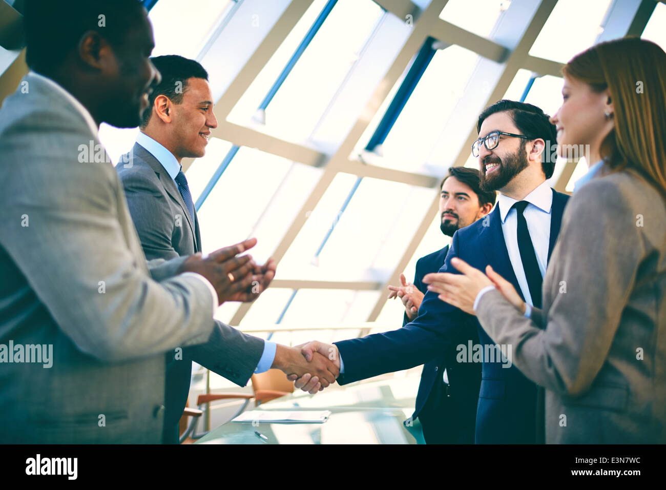 Two successful businessmen handshaking while their colleagues clapping ...