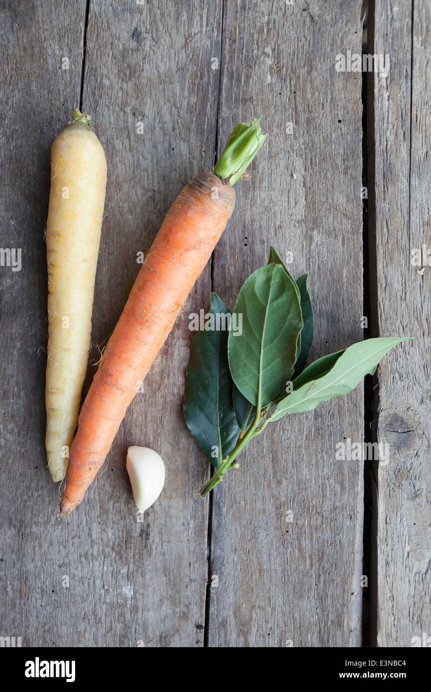 Root vegetables with bay leaves and garlic clove on wooden table Stock ...