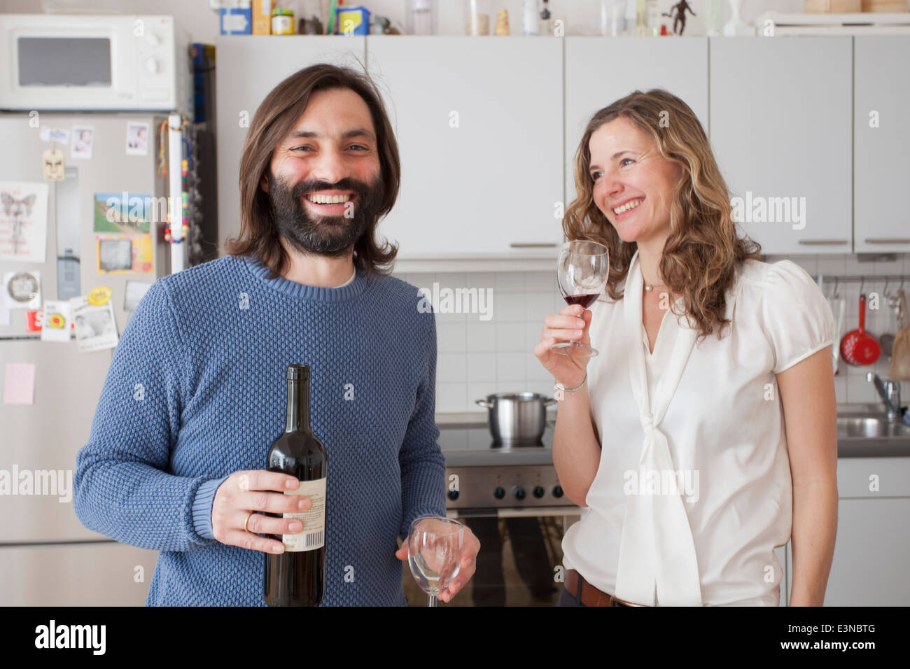 Happy couple enjoying red wine in kitchen Stock Photo - Alamy