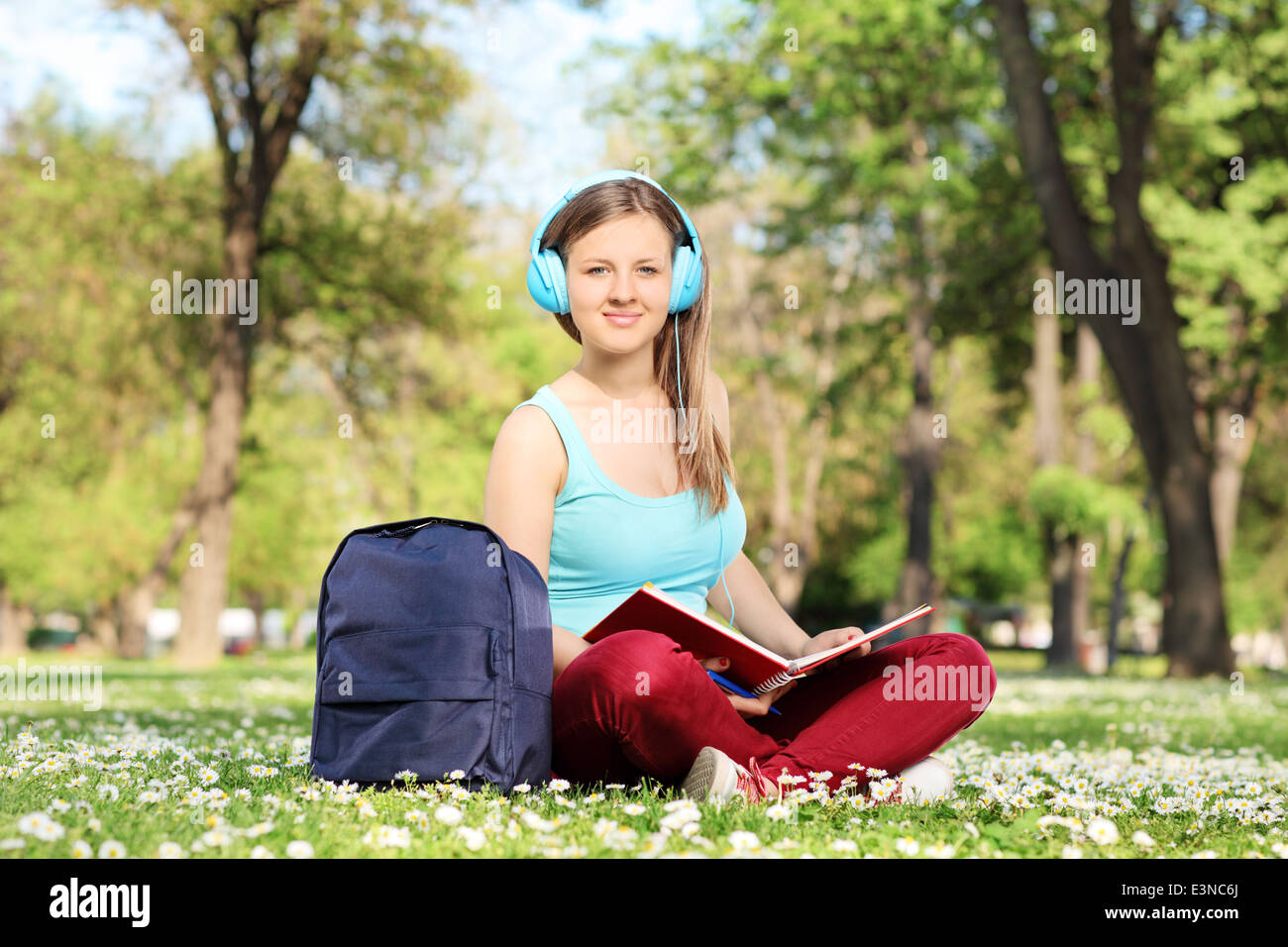 Girl studying in park and listening to a music seated in a field full ...