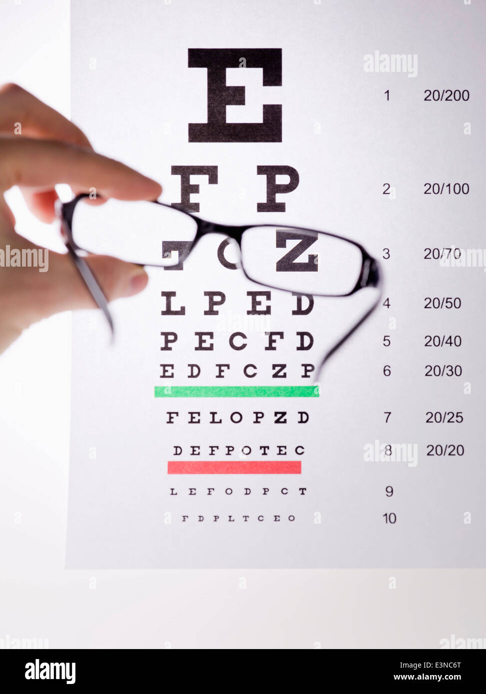 Hand holding glasses in front of eye exam chart Stock Photo - Alamy