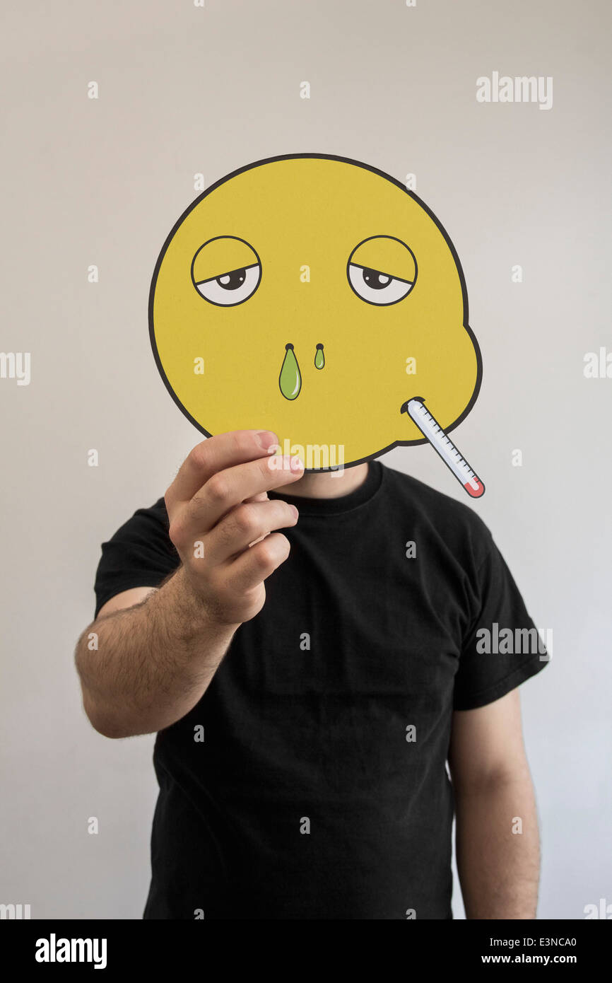 Man holding a sick emoticon face in front of his face Stock Photo - Alamy