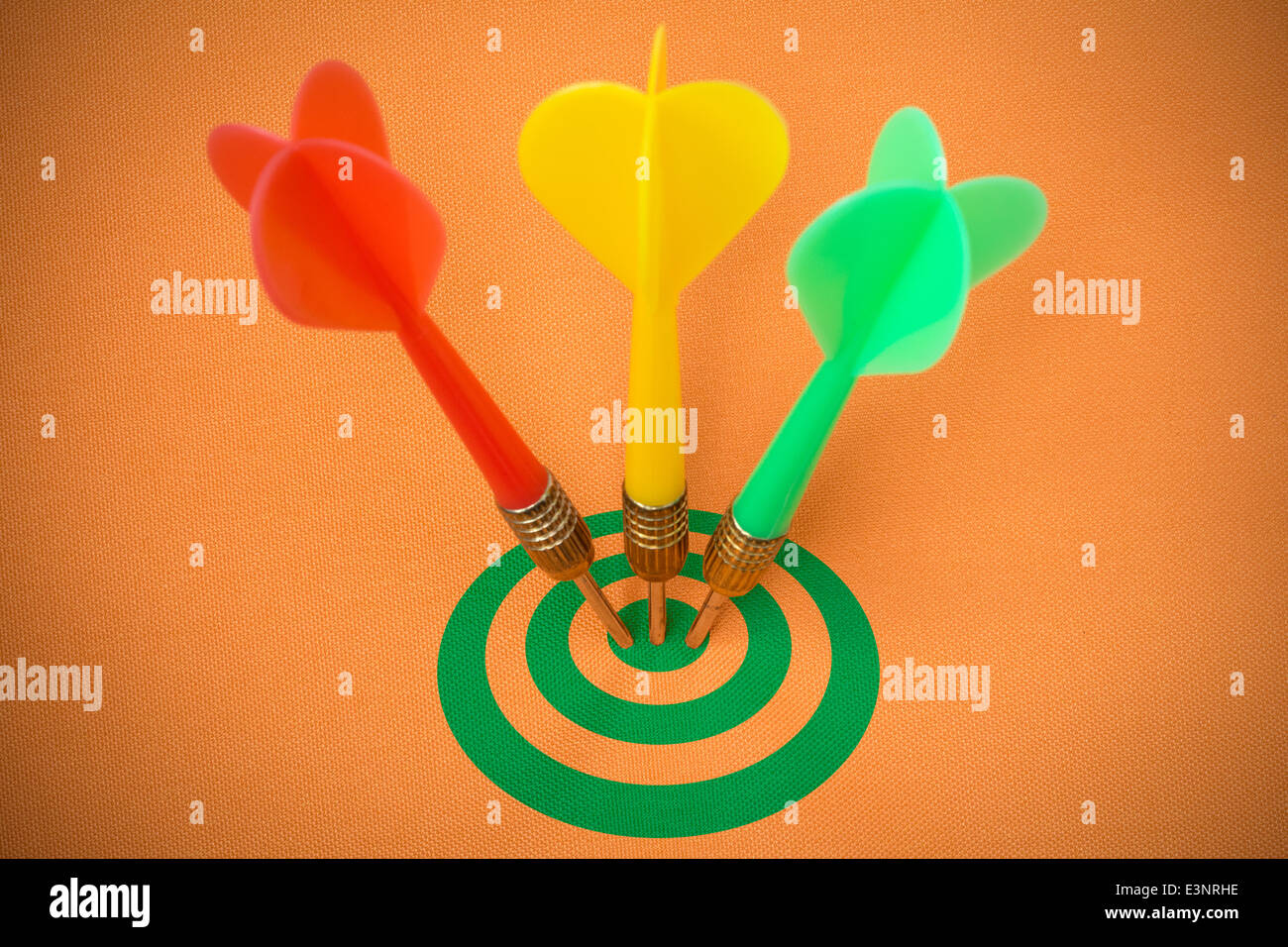 Three darts hitting green target on orange background Stock Photo - Alamy