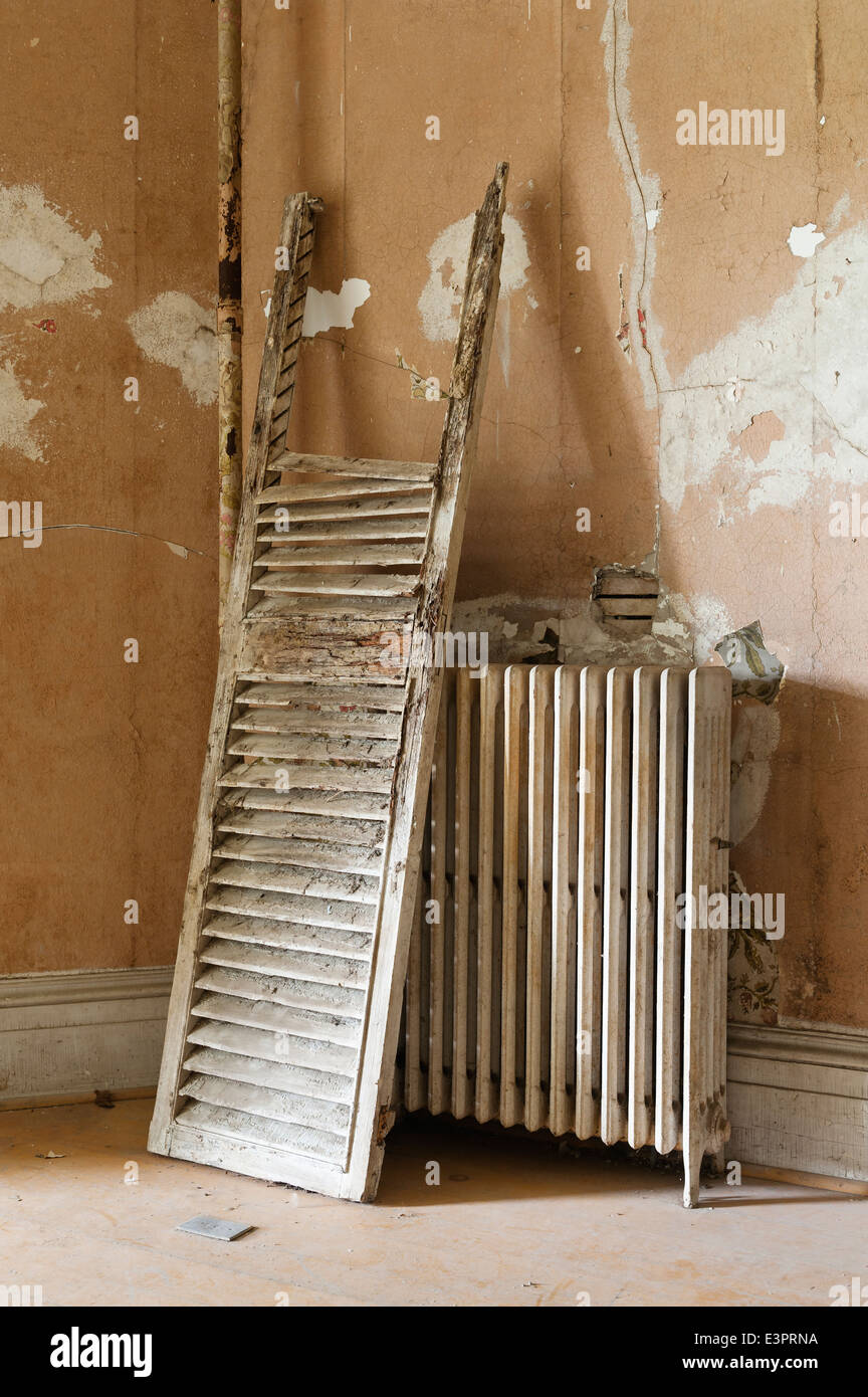 Damaged old shutter leaning against an old iron radiator by wall with ...