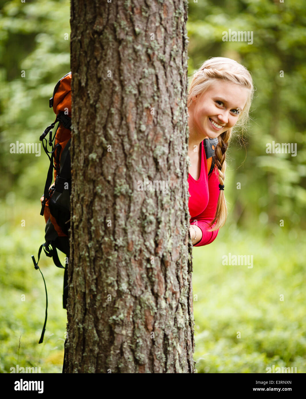 Young blond woman hiking and hiding behind a tree in the forest Stock ...