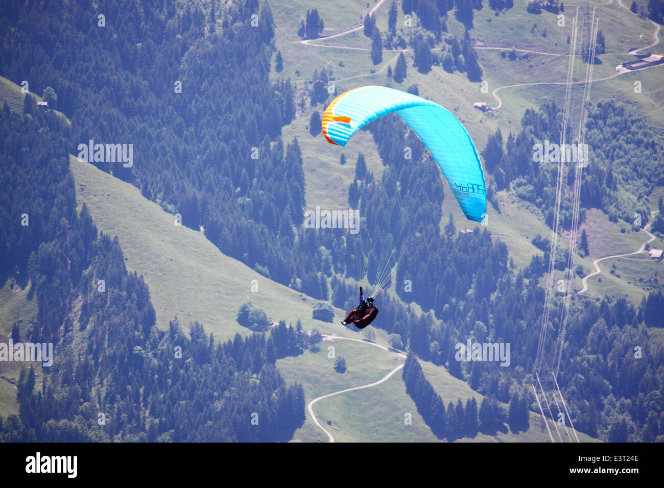 A blue paraglider with forests and fields and power lines in the ...