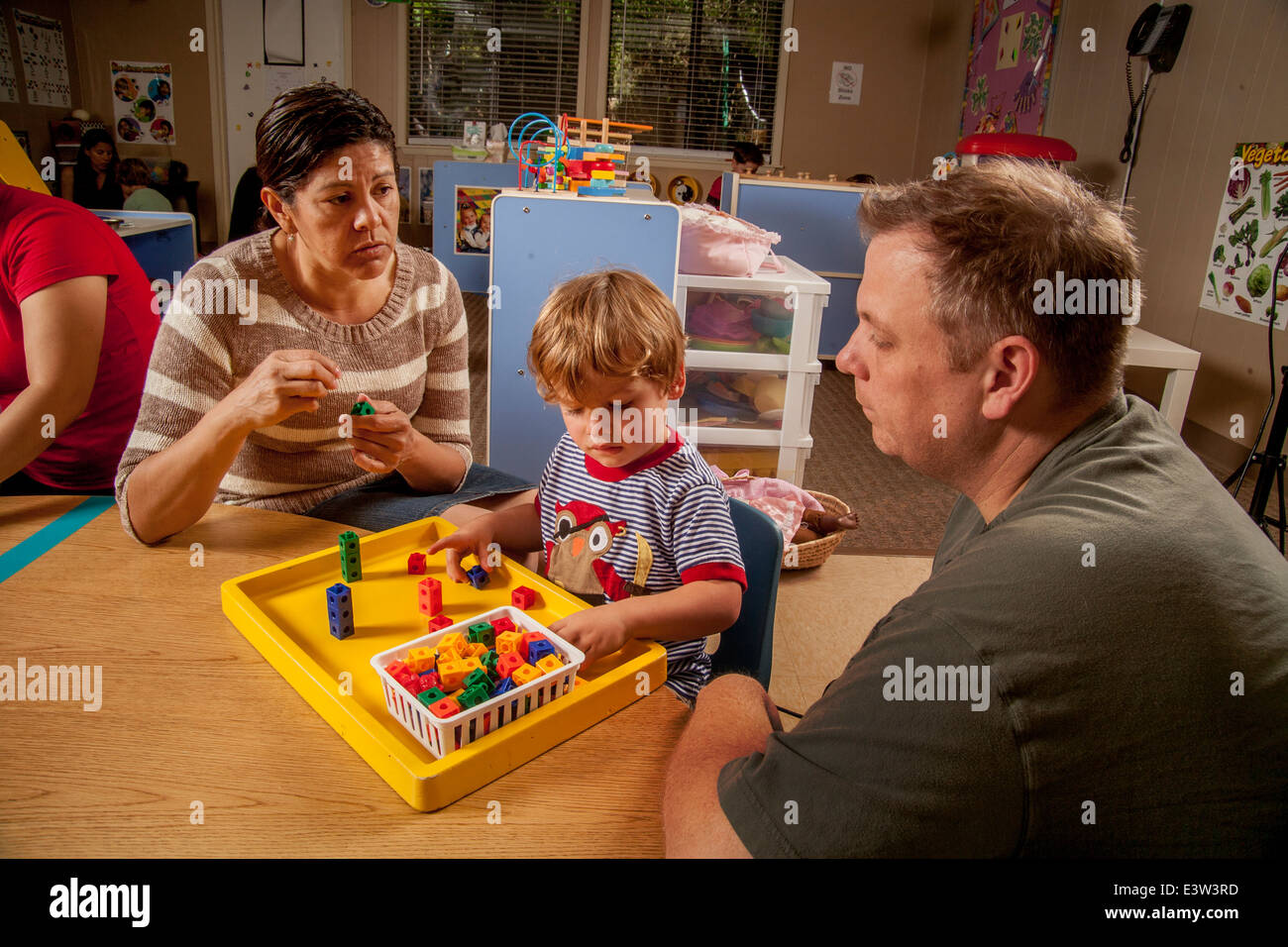 A Hispanic teacher uses visual learning aids aids with a young boy ...
