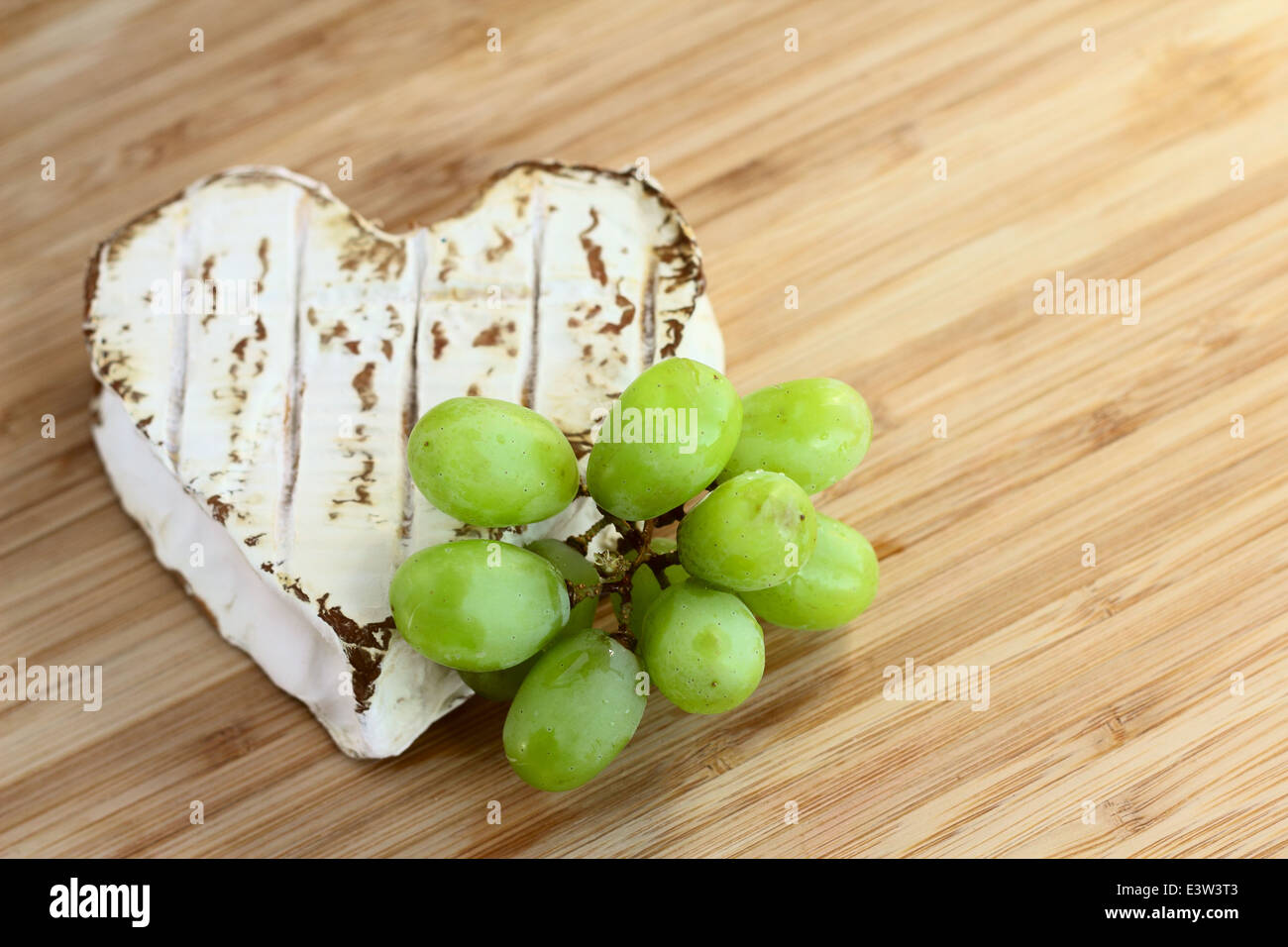 Neufchatel cheese shaped like heart with grapes on wooden cutting board ...