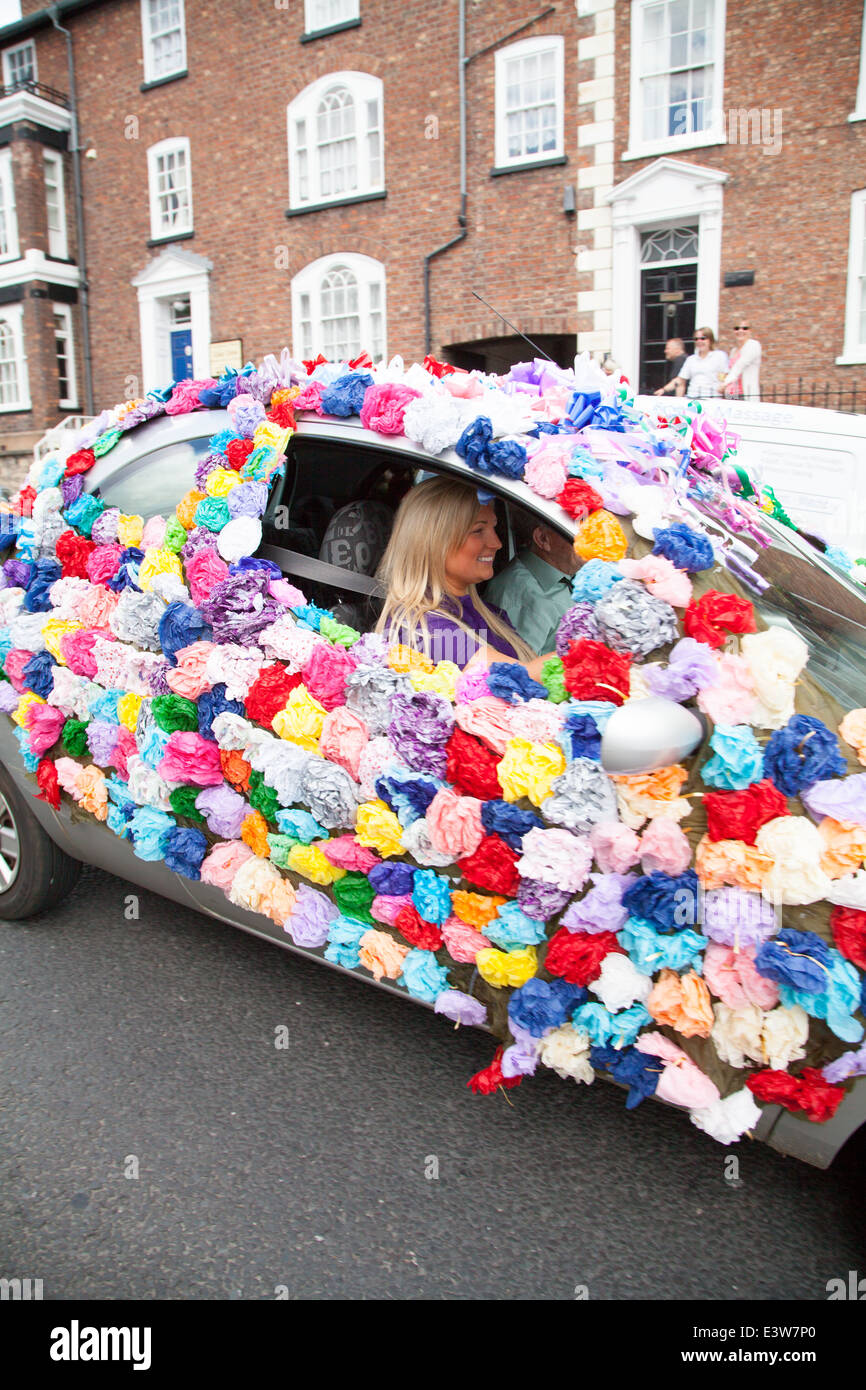 A young blonde woman driving a small car covered in paper rosettes ...