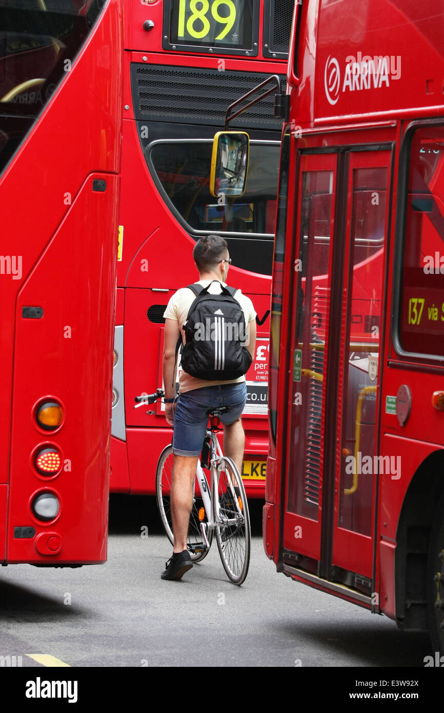 A cyclist waiting amongst a queue of red London double decker buses in ...