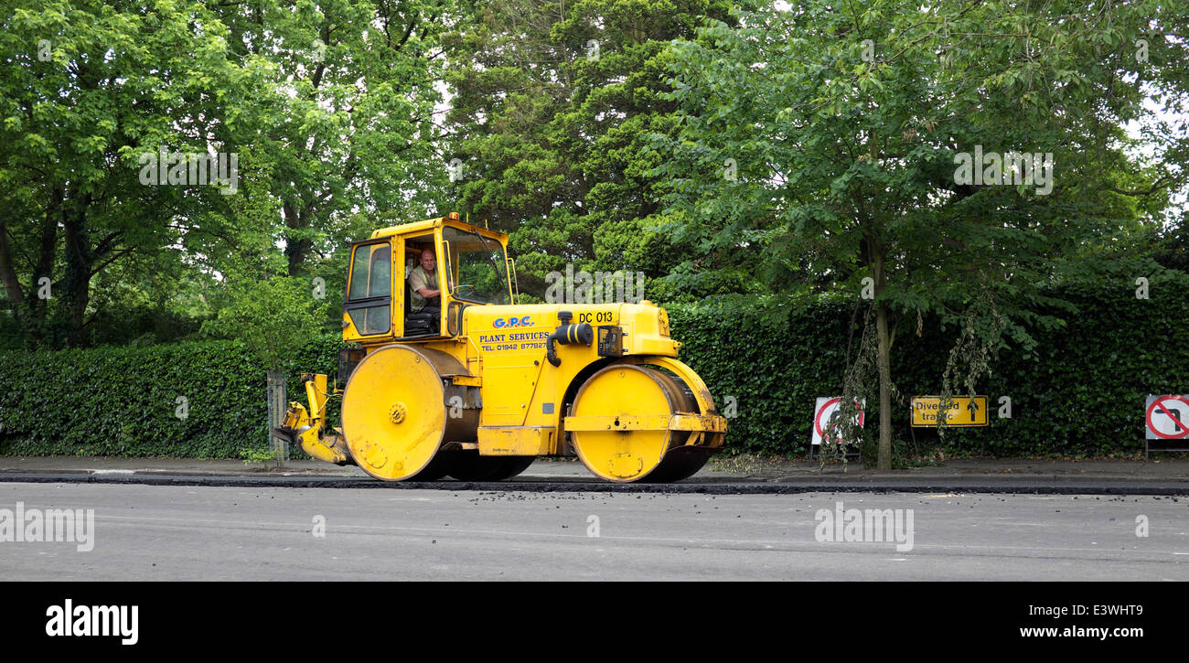 a steamroller flattens newly laid tarmac to repair a road damaged by ...