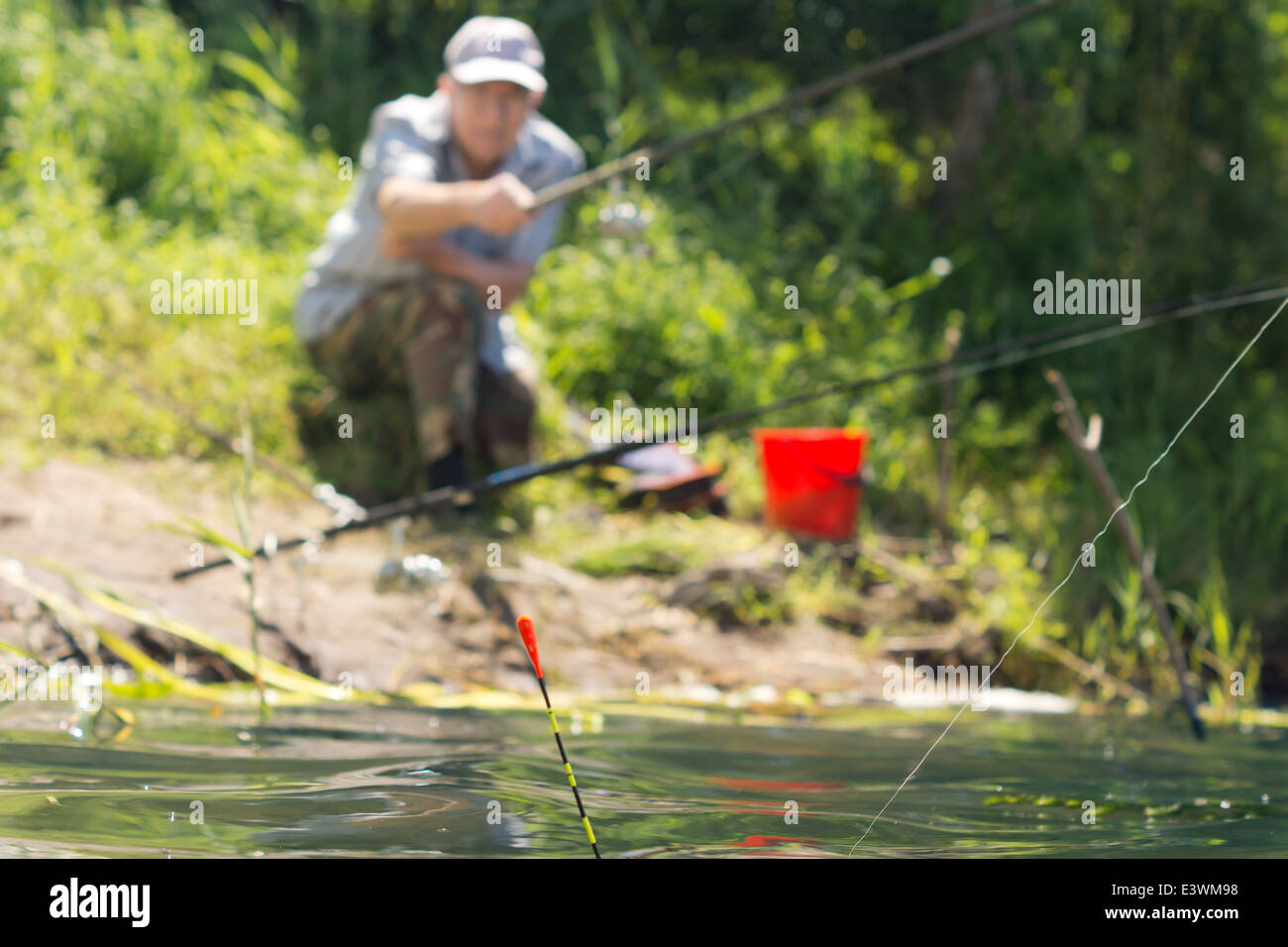 Man fishing at the edge of a lake with focus to his line and the ...