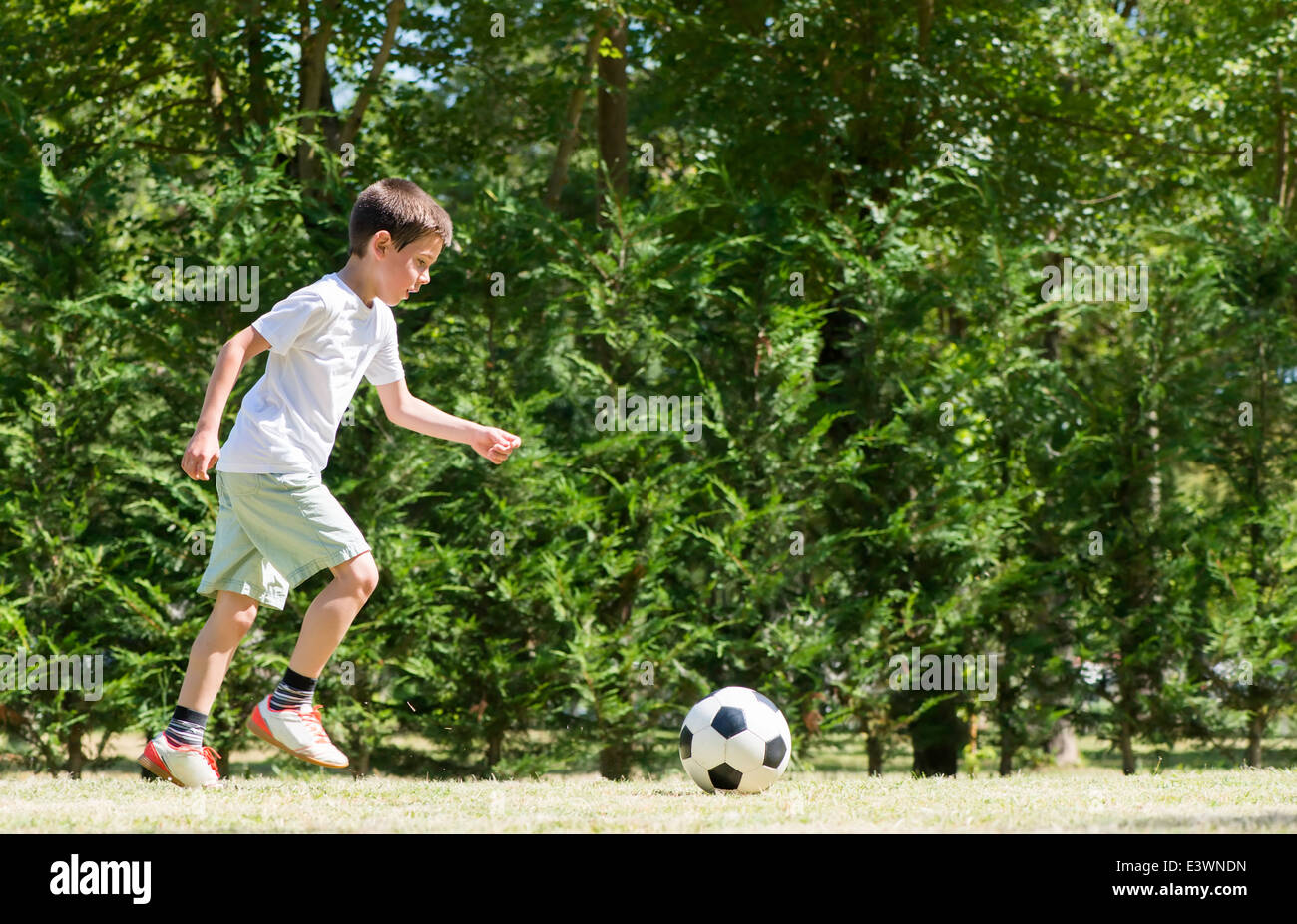 Child playing football in a stadium. Trees on the background Stock ...