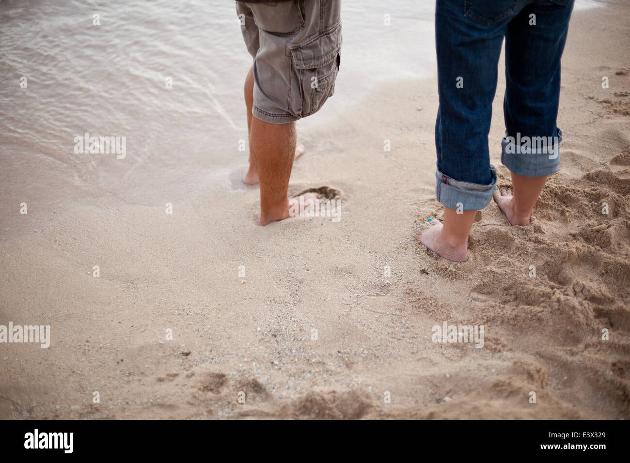 Feet standing in sand by lapping waves Stock Photo - Alamy