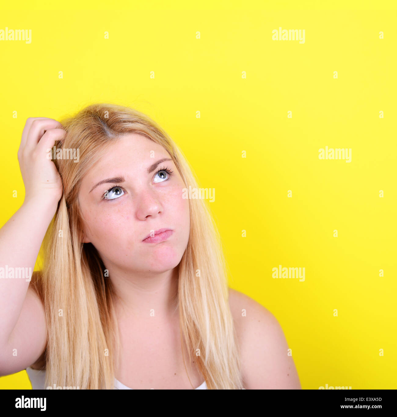 Portrait of beautiful girl thinking and looking up against yellow ...