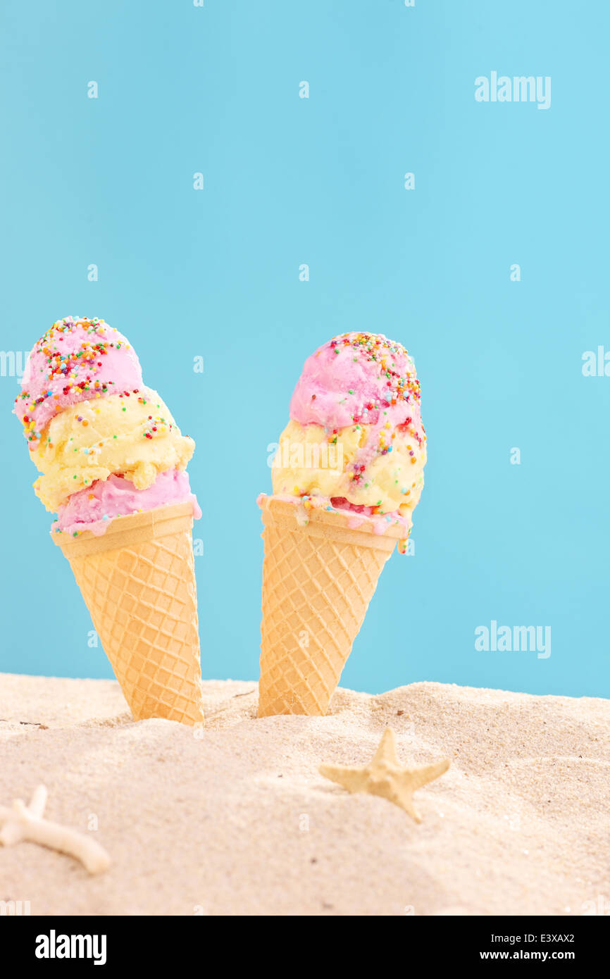 Vertical shot of two ice creams stuck in sand on blue background Stock ...