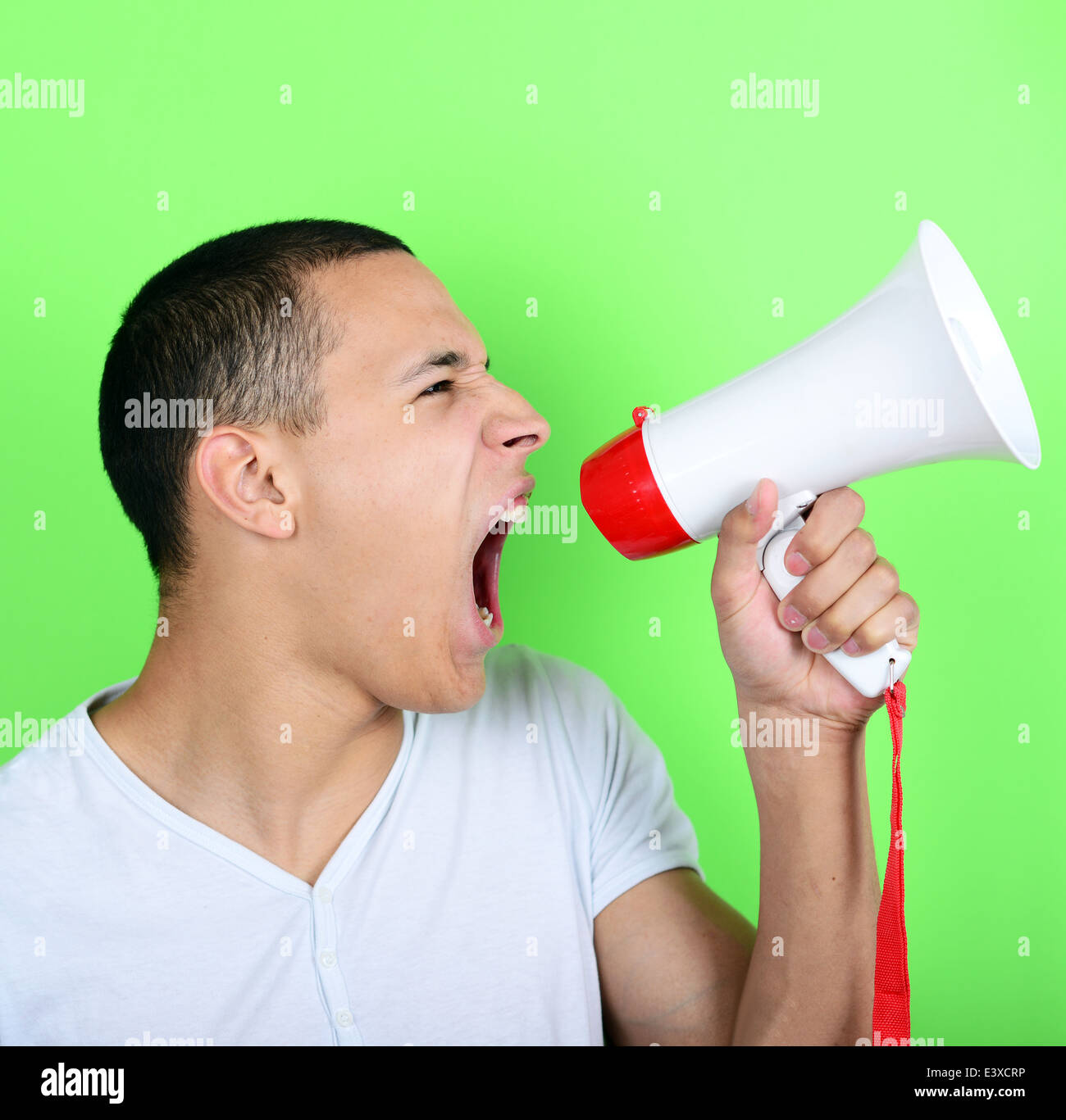 Portrait of young man shouting with a megaphone against green ...