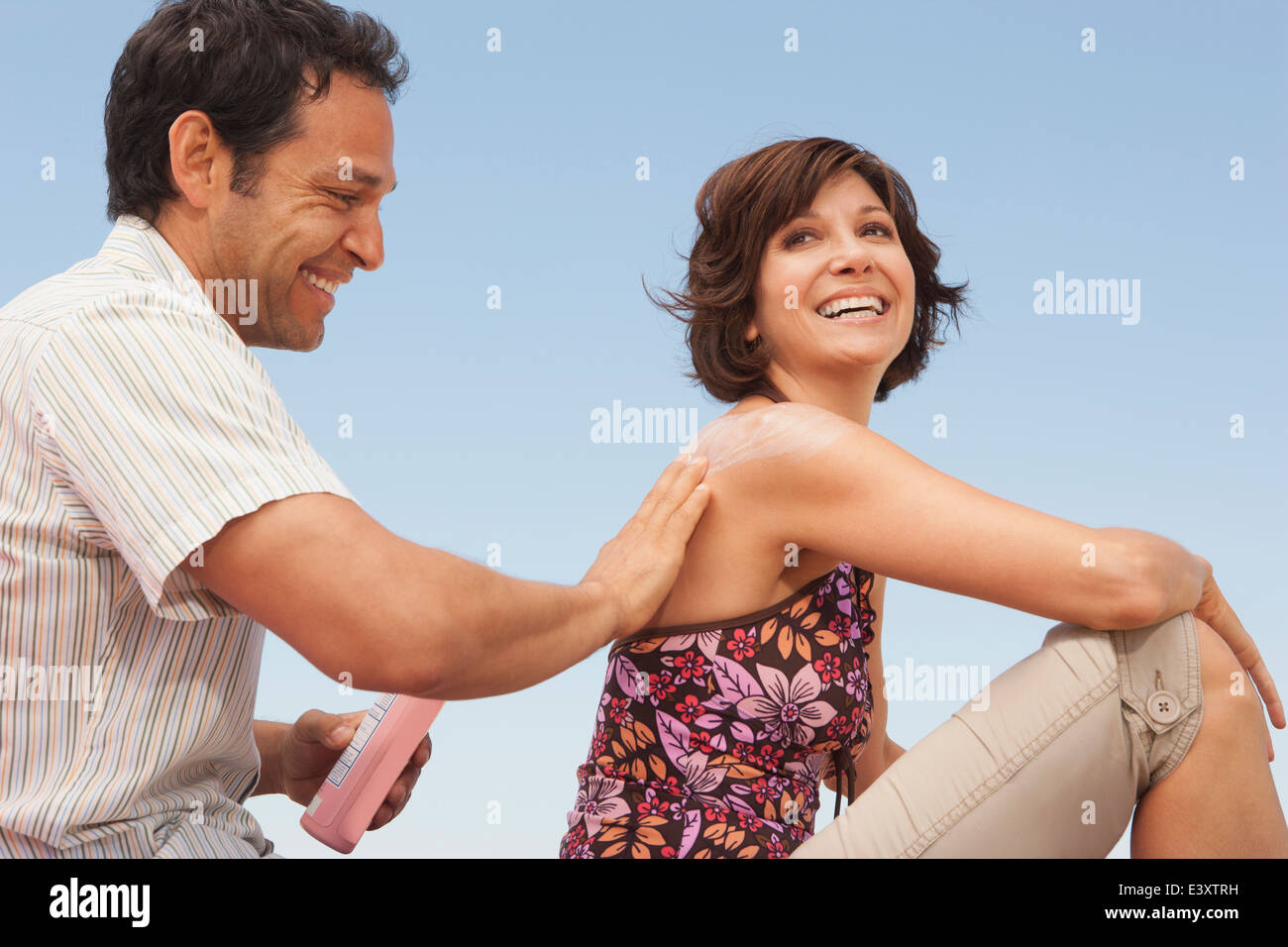 Man rubbing sunscreen on girlfriend's shoulders Stock Photo - Alamy