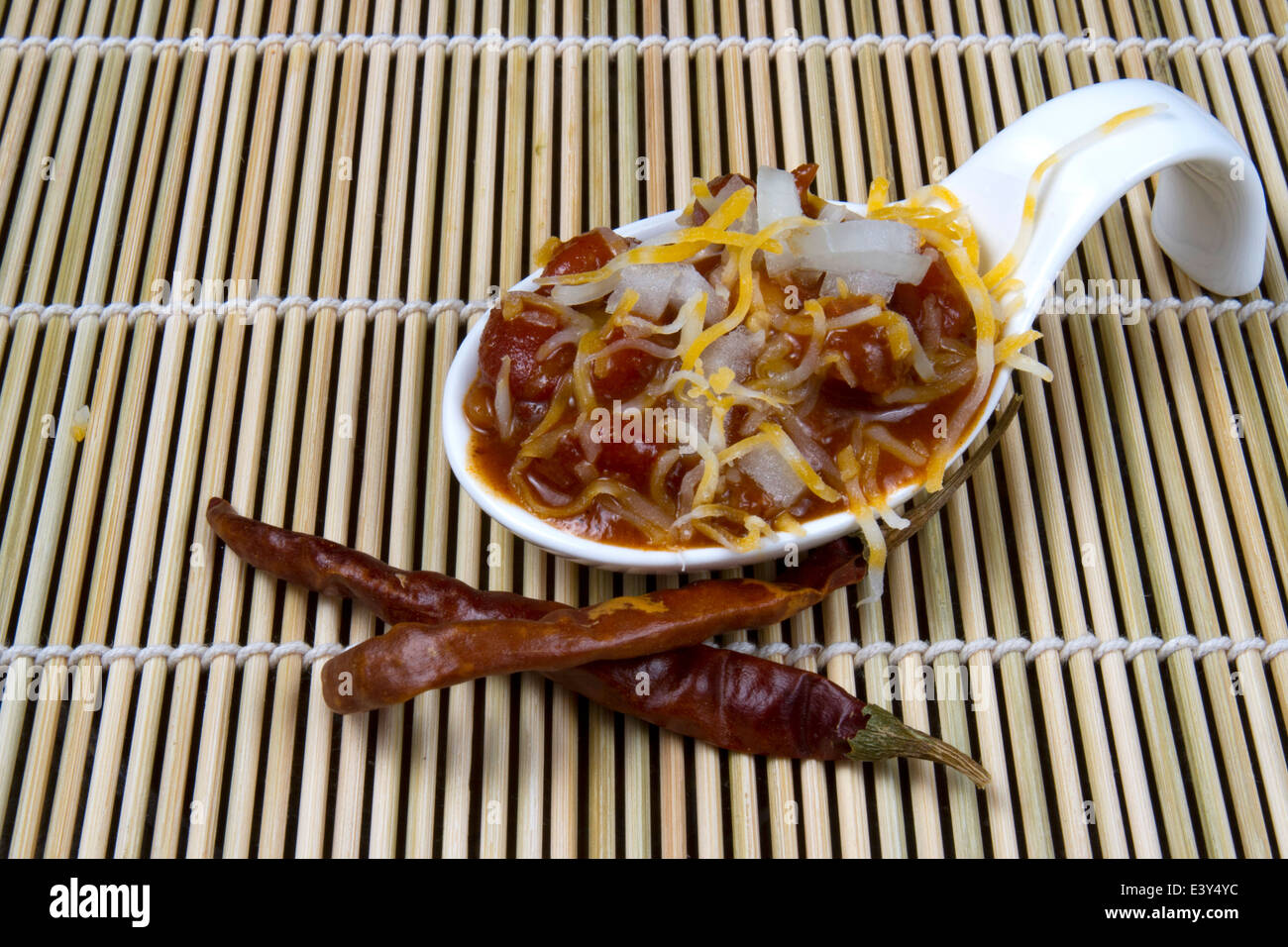 Chili con carne in white tasting spoon covered in cheese and onions ...