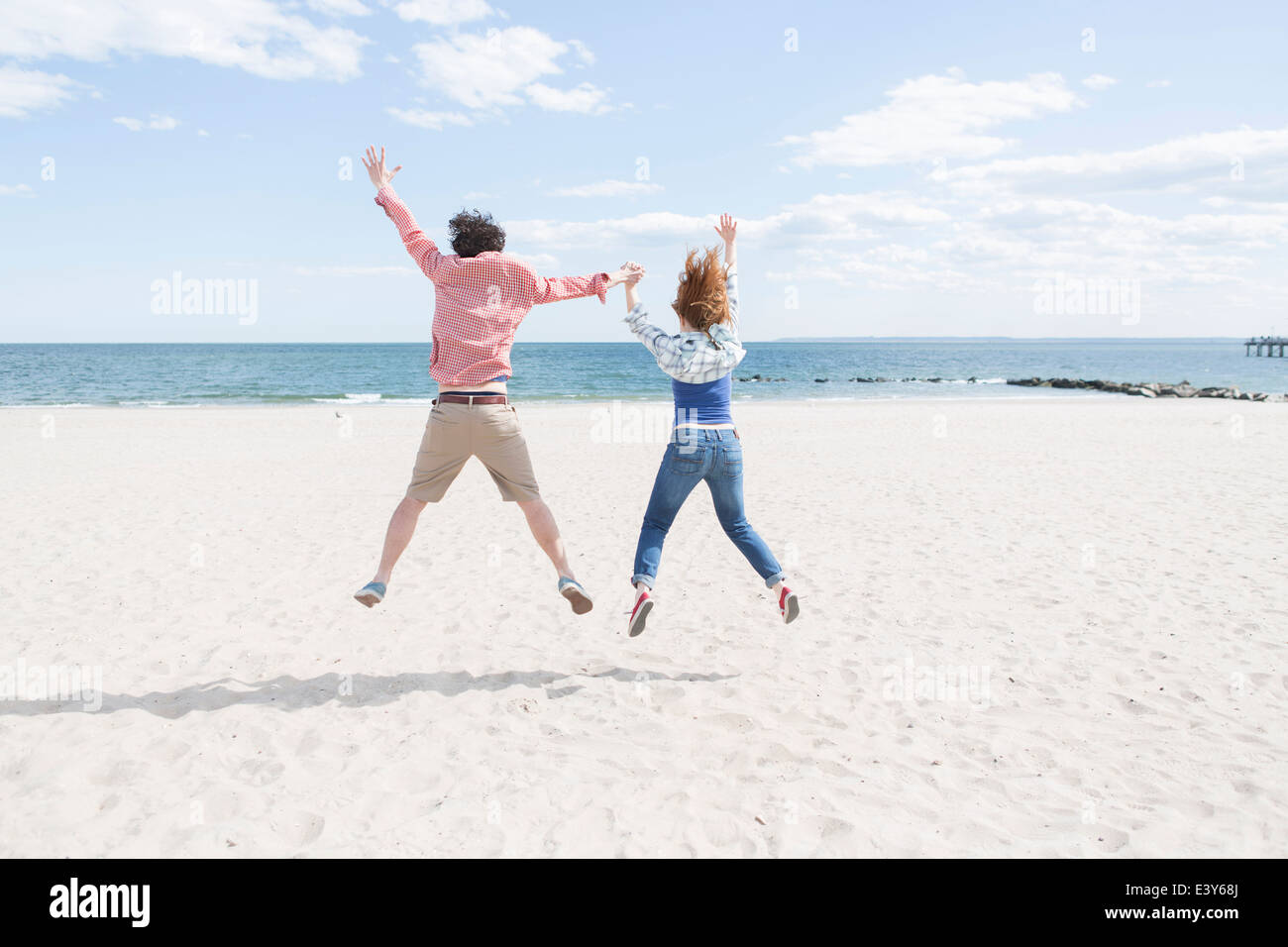 Rear view of couple jumping mid air on beach Stock Photo - Alamy