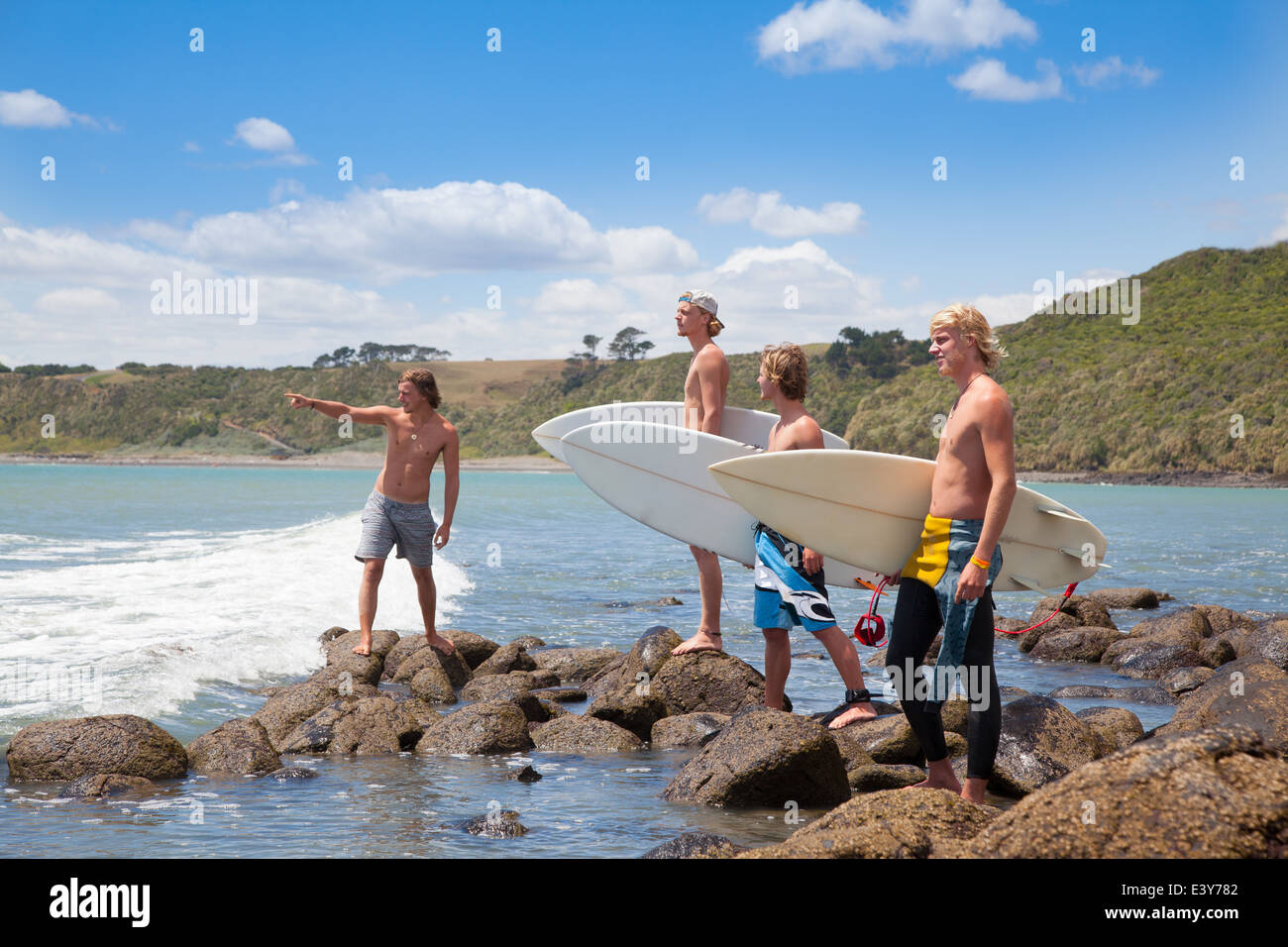 Four young male surfer friends pointing to sea from rocks Stock Photo ...