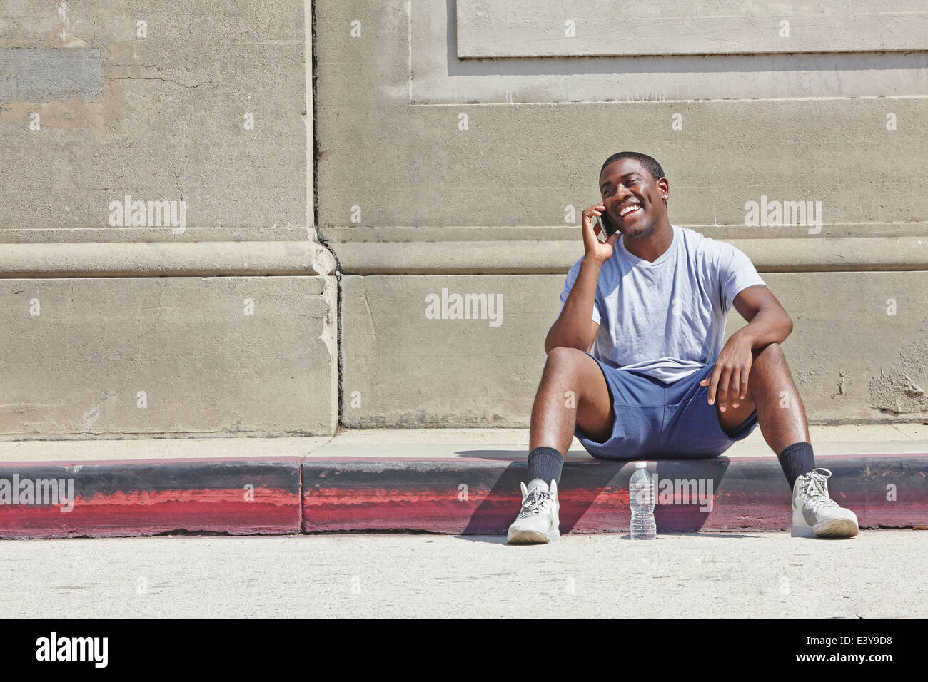 Young male runner sitting on sidewalk chatting on smartphone Stock ...