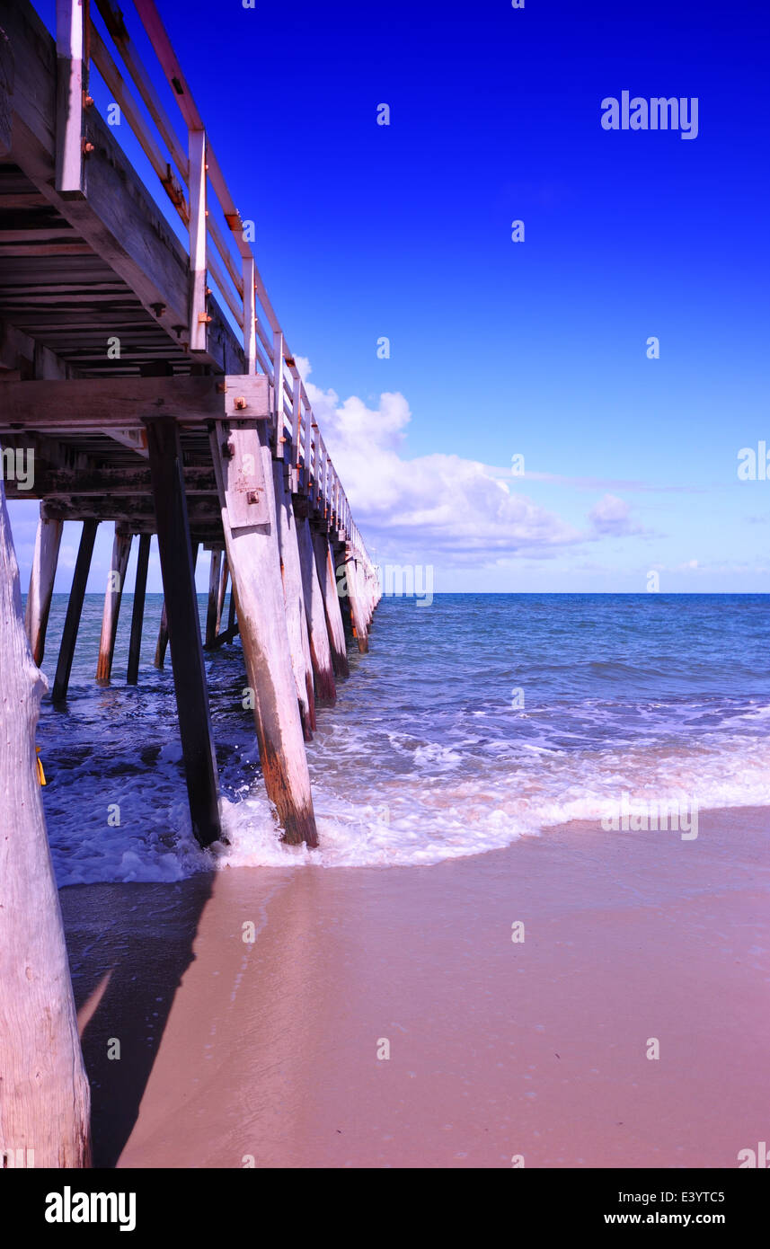 Side view of long jetty pier on sandy beach with ocean and blue skies ...
