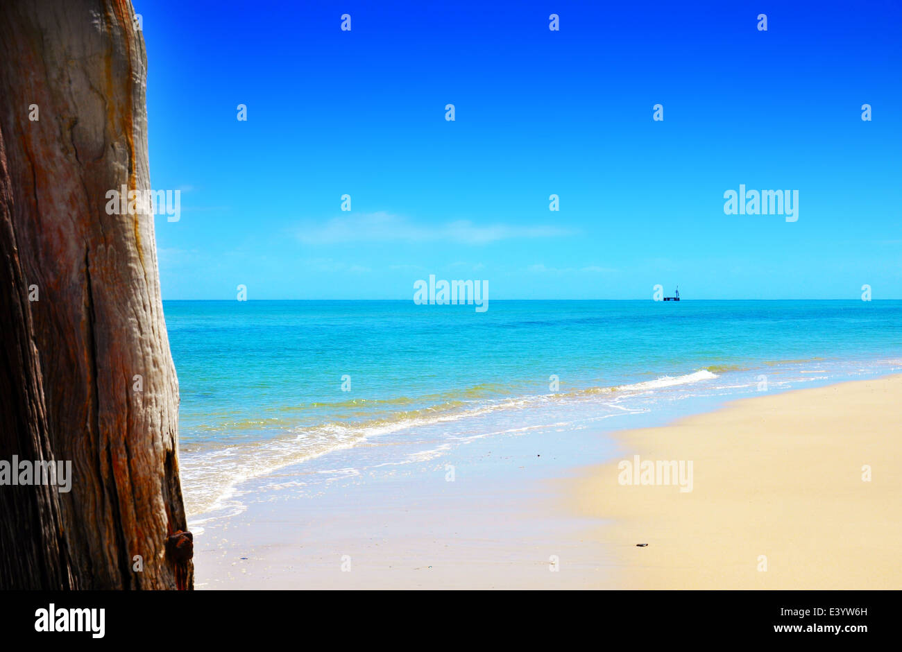 Wide sandy beach with blue skies and calm ocean with jetty pylon in ...