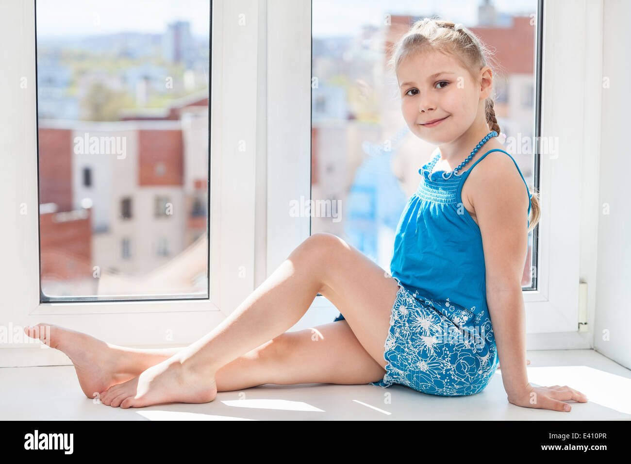 Girl in blue dress sitting on window sill in sun light Stock Photo - Alamy