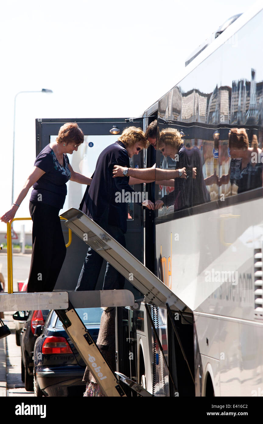 Disabled elderly people getting on to tour bus aided by hydraulic lift ...