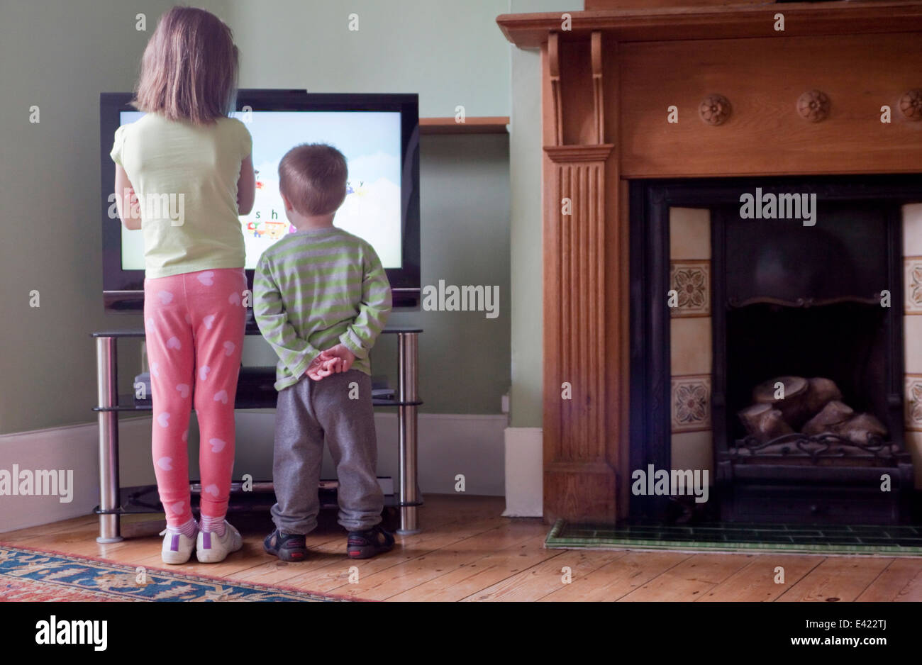Rear view of sister and brother standing too close to and watching TV ...