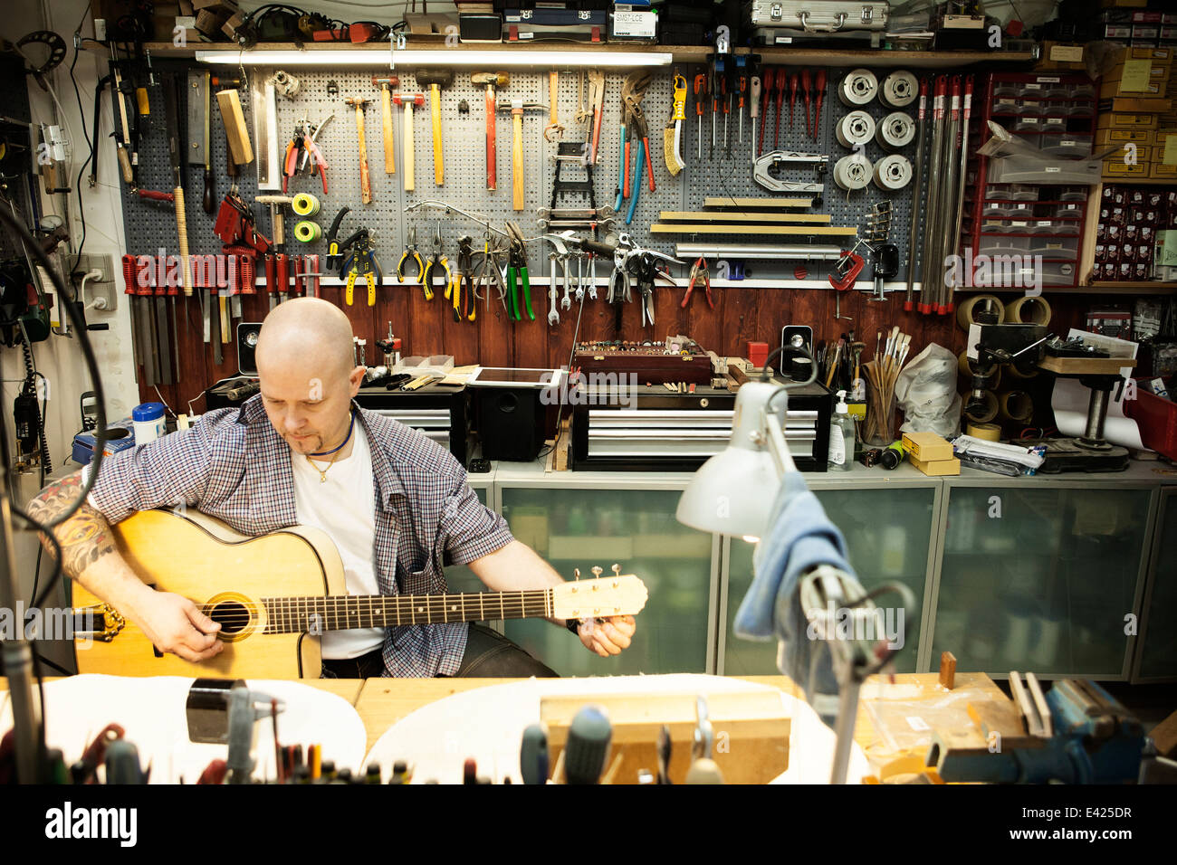 Guitar maker tuning acoustic guitar in workshop Stock Photo - Alamy