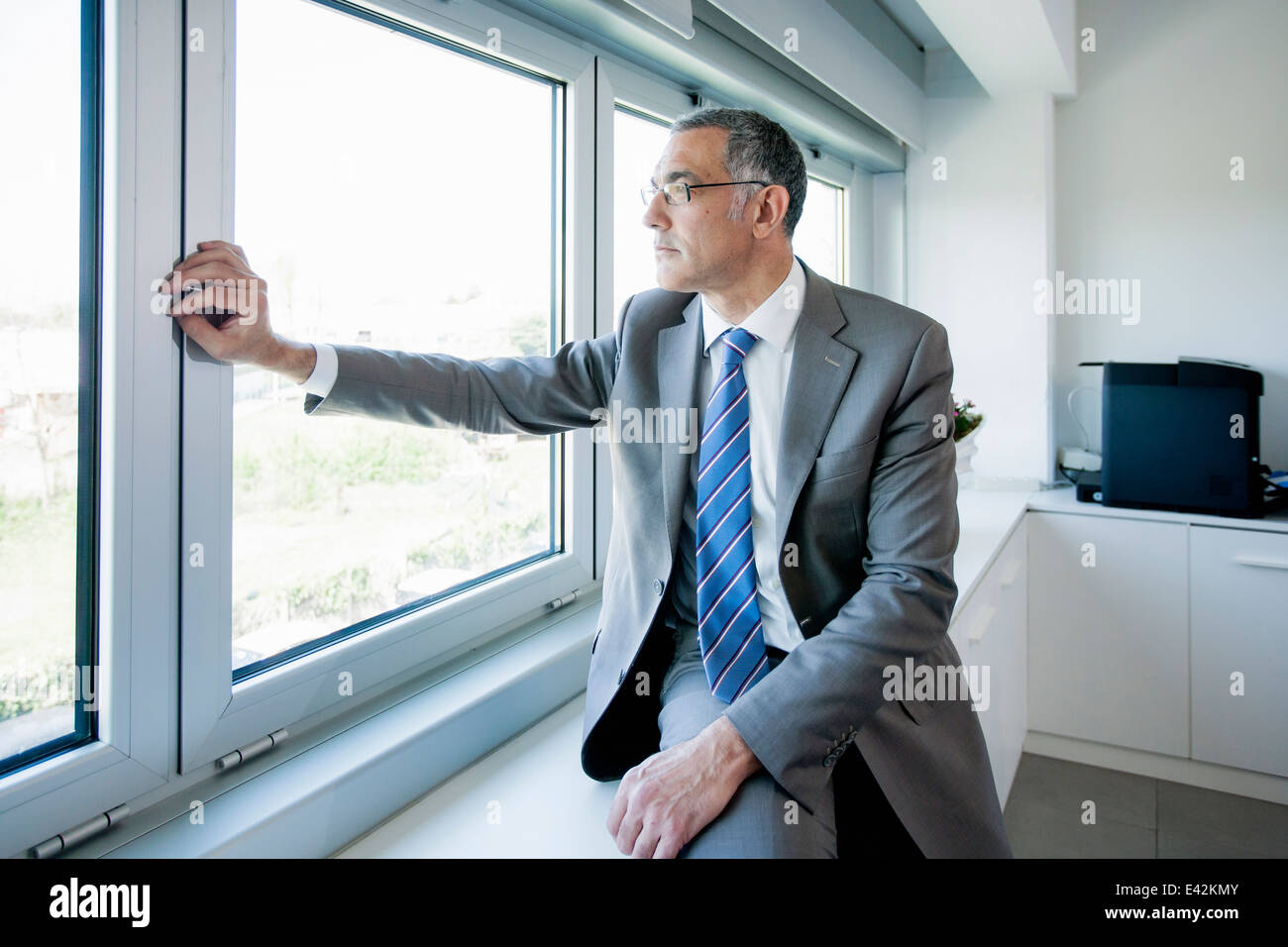 Businessman looking out of office window Stock Photo - Alamy