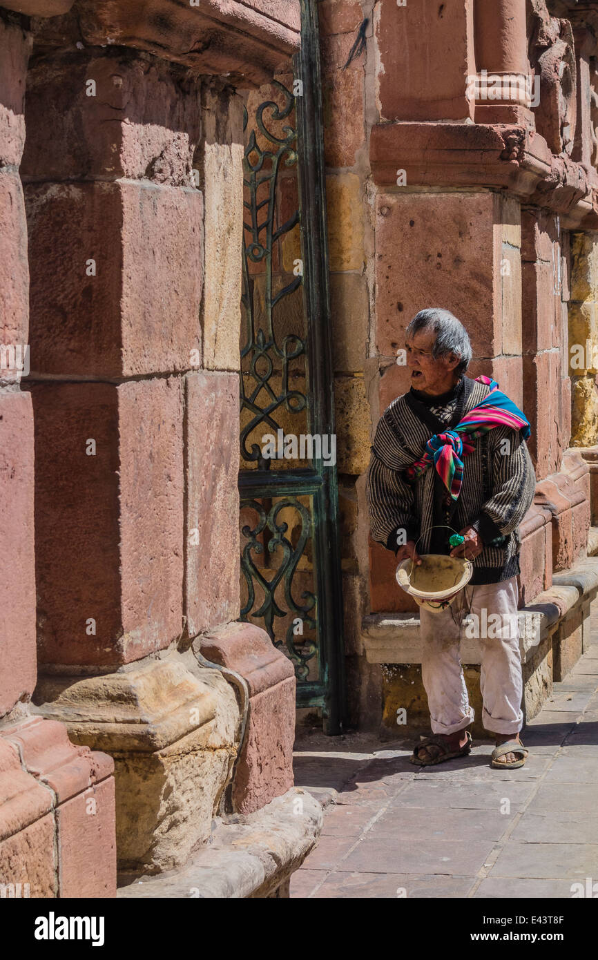 An older indigenous Bolivian man holds his hat out to collect money as ...