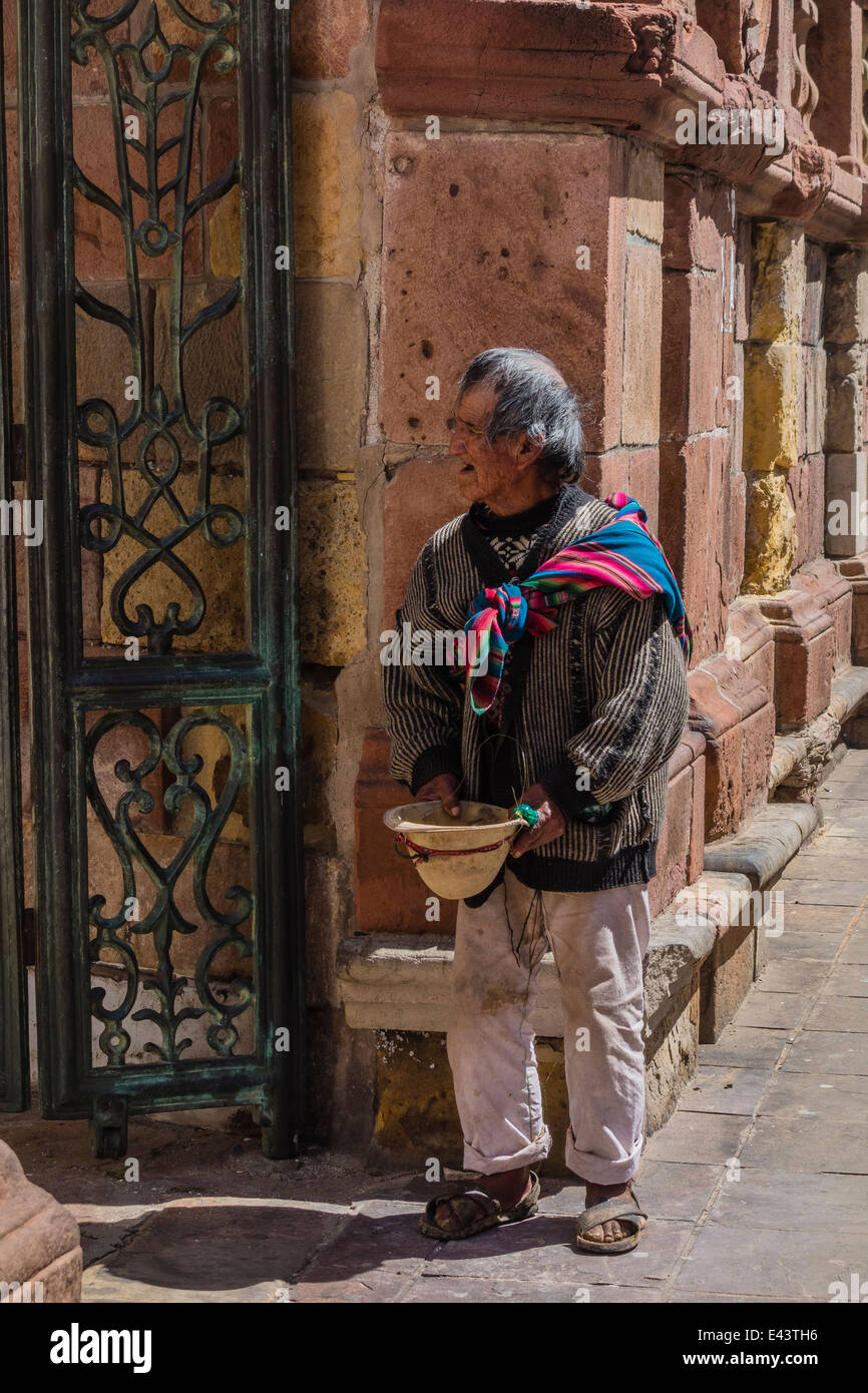 An older indigenous Bolivian man holds his hat out to collect money as ...