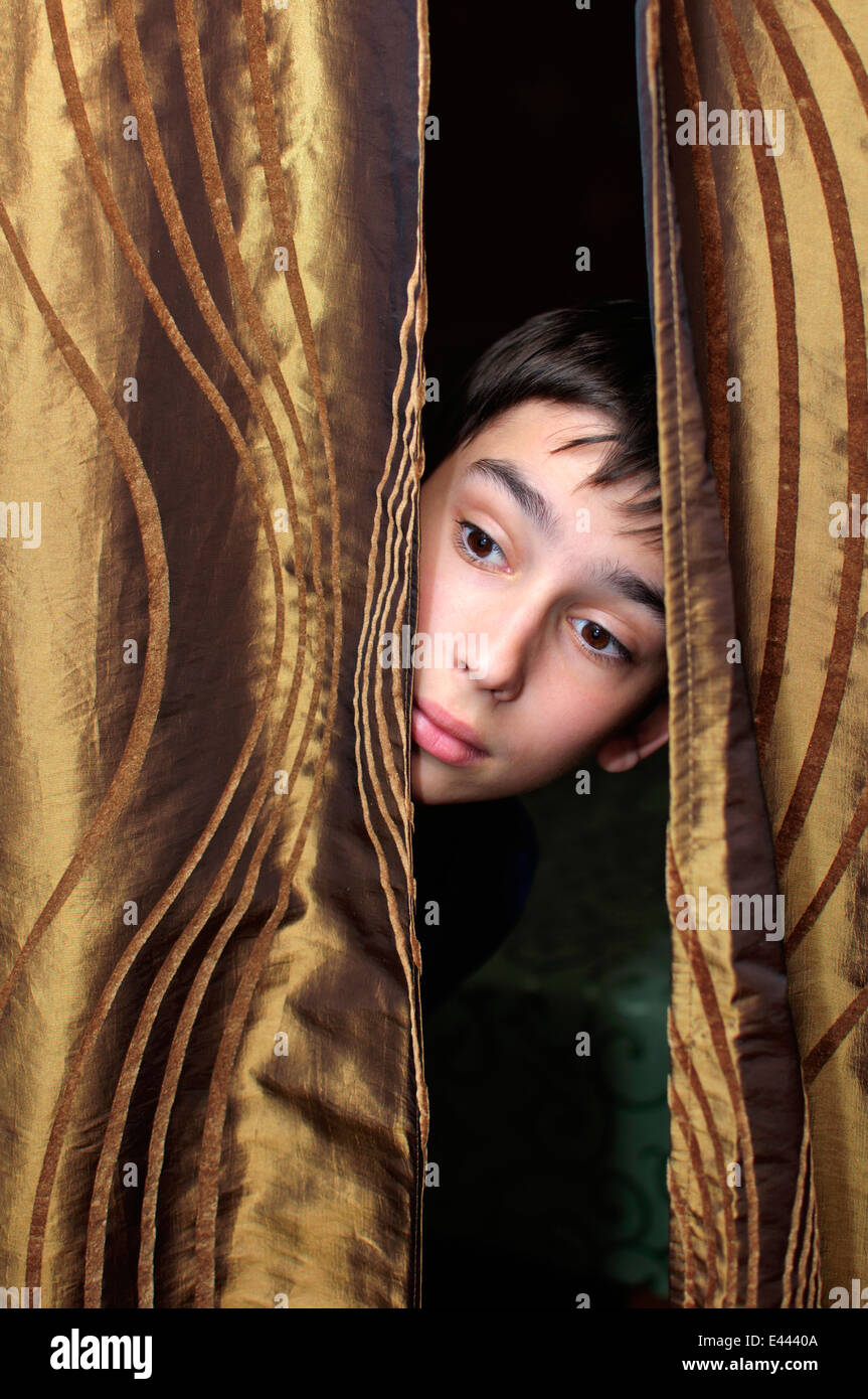 Boy looks out from behind the curtain Stock Photo - Alamy