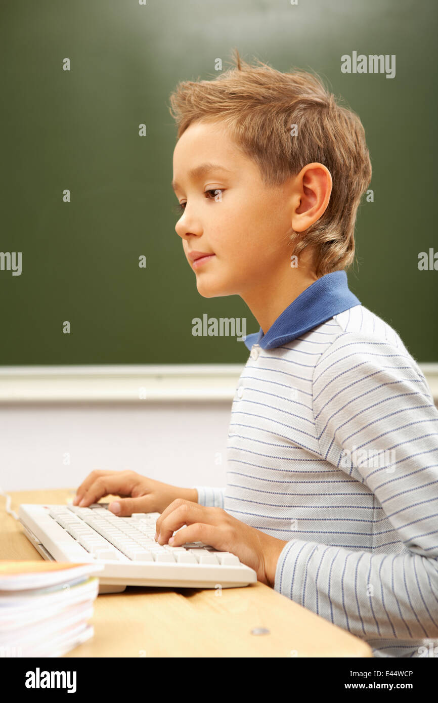 Portrait of cute lad typing on computer board in classroom Stock Photo ...
