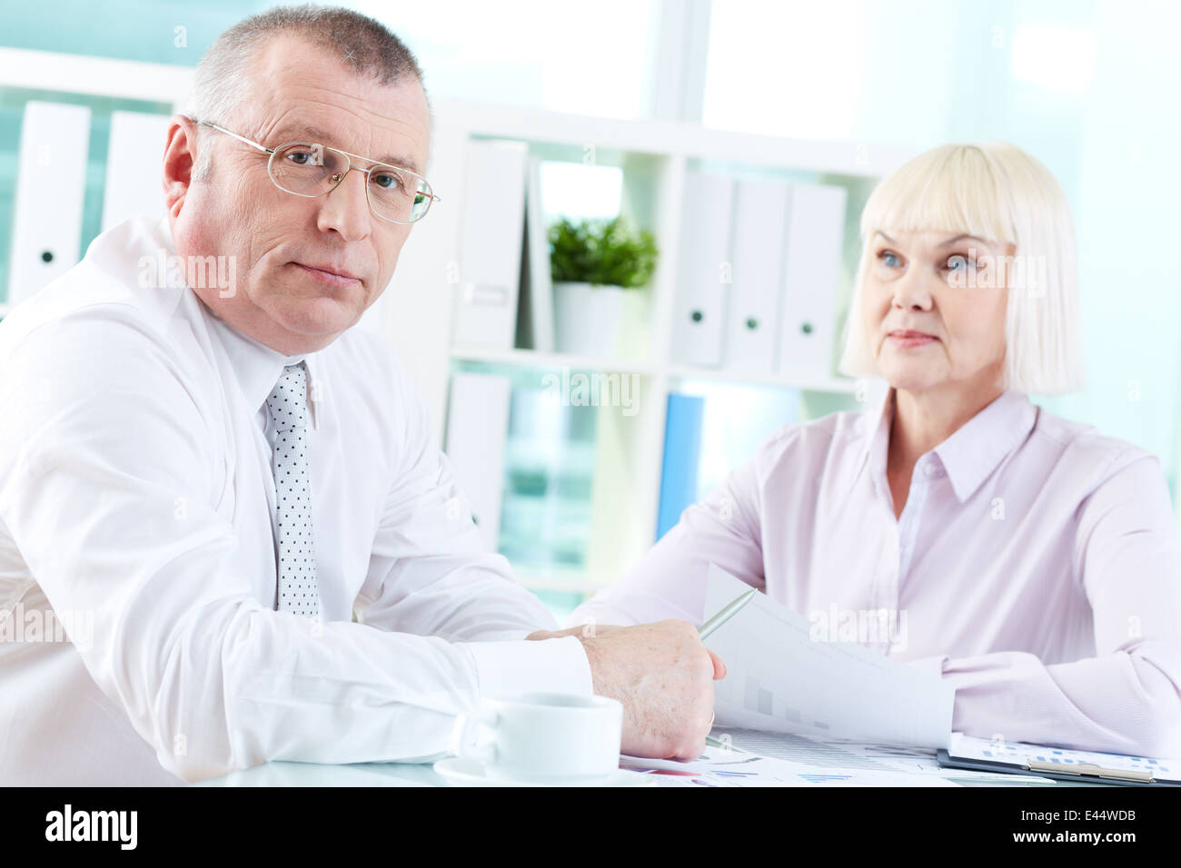 Portrait of serious boss looking at camera at workplace with mature ...