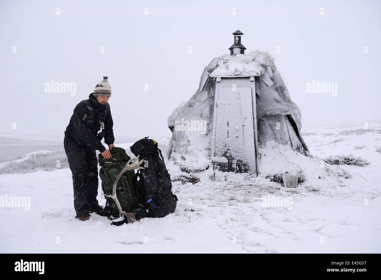 Photographer, Vincent Munier, outside small hut with rucksacks in snow ...