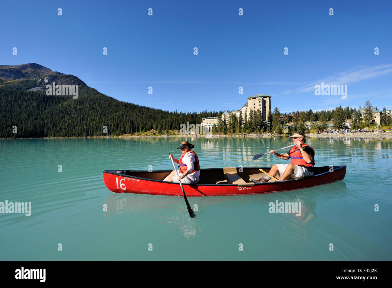 Two people canoeing on Lake Louise, a hotel on the shore, Banff ...