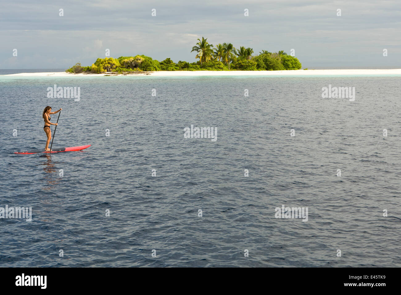 Woman paddle boarding around small uninhabited island, Ari Atoll ...