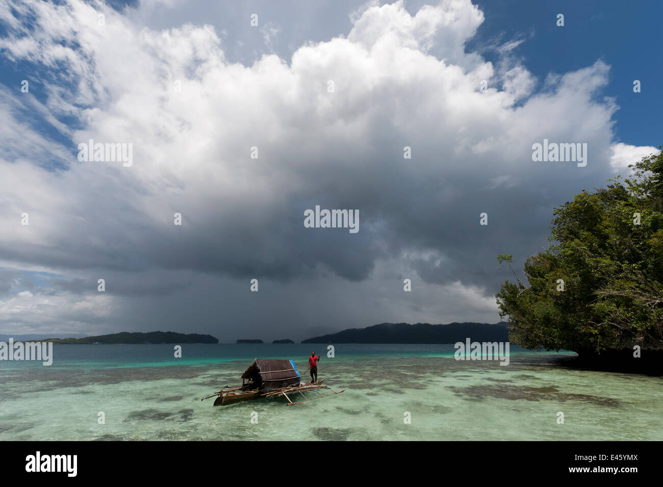 West Papuan fisherman in his outrigger house boat in the shallows over ...