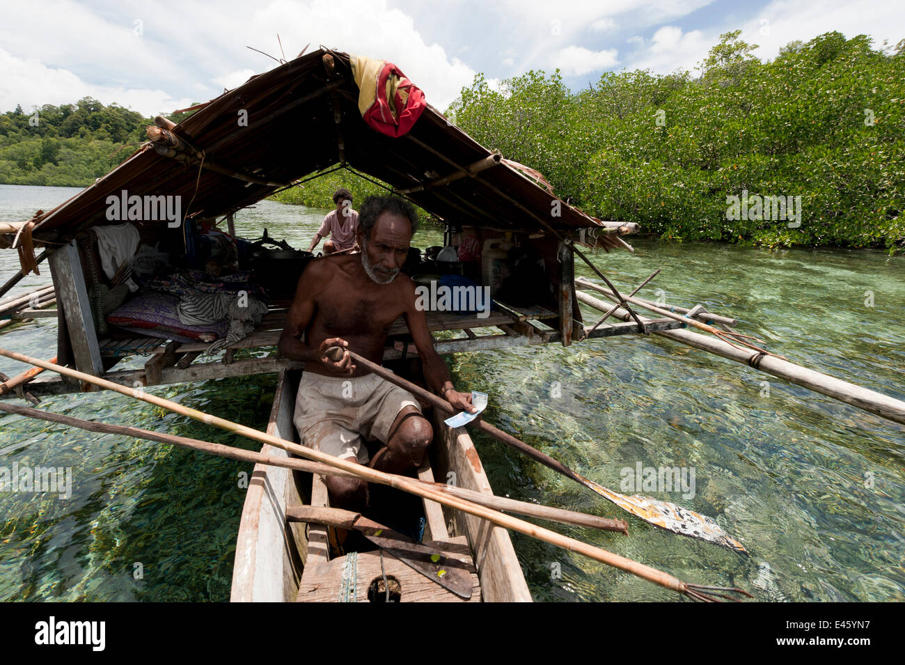 West Papuan fisherman paddling in a traditional outrigger house boat ...