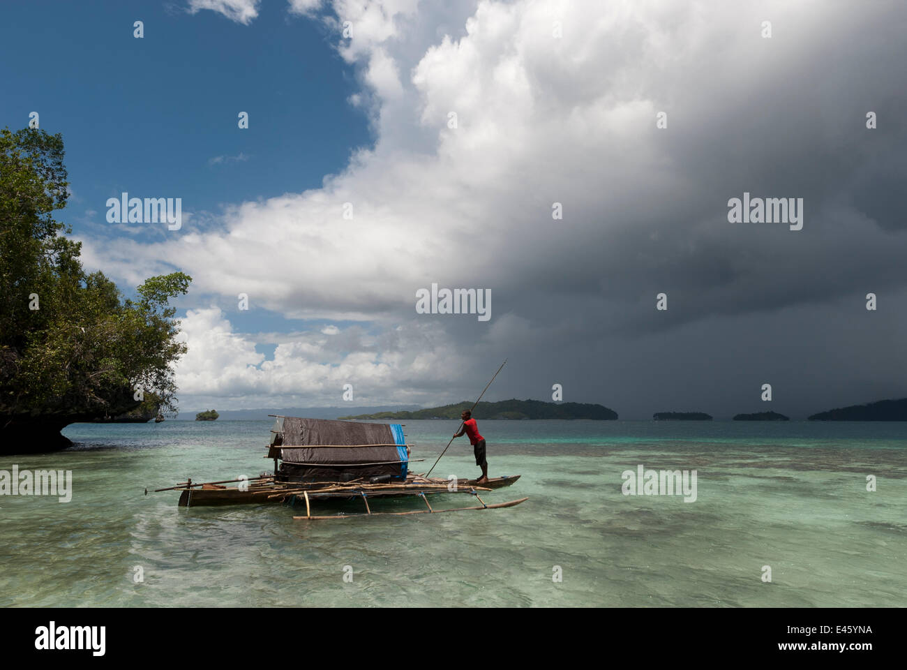 West Papuan fisherman in his outrigger house boat leaving the shallow ...