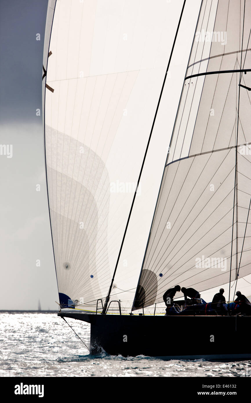 Crew member silhouetted against white spinnaker on board yacht during ...
