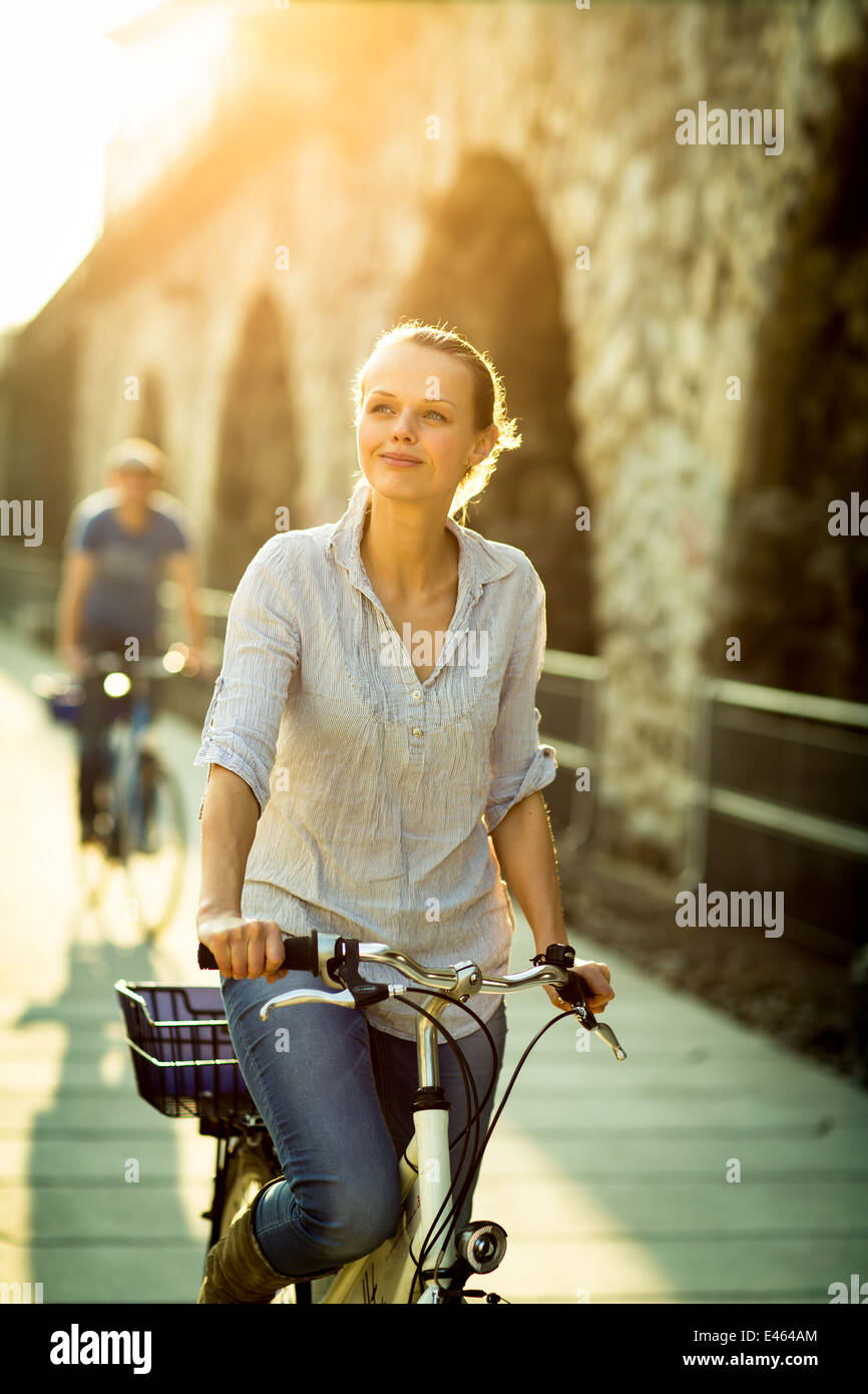 Pretty, young woman riding a bicycle in a city with her boyfriend ...